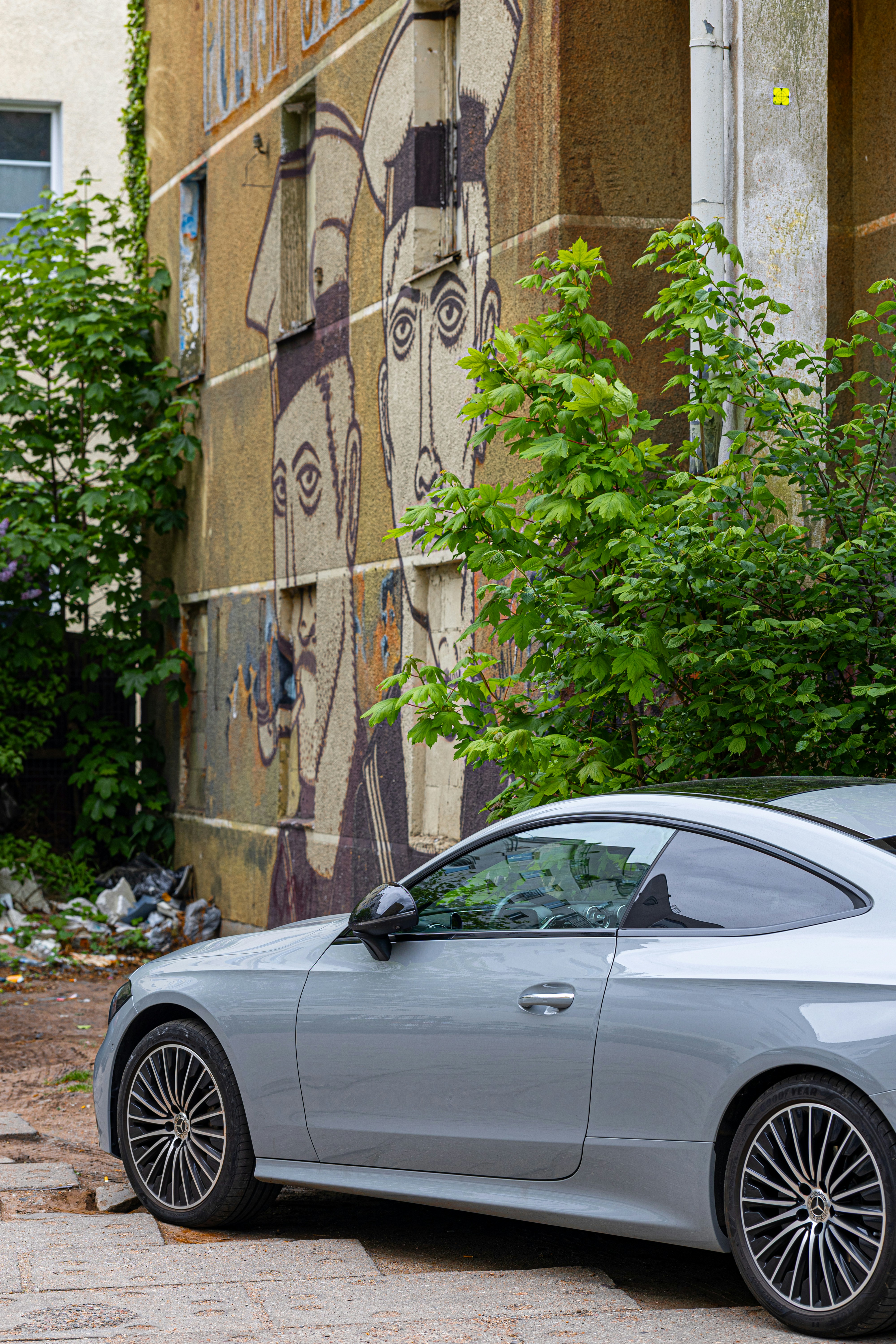 Graffito Portraits Meet Urban Quiet: A Silver Coupe in Front of Colorful Wall Art