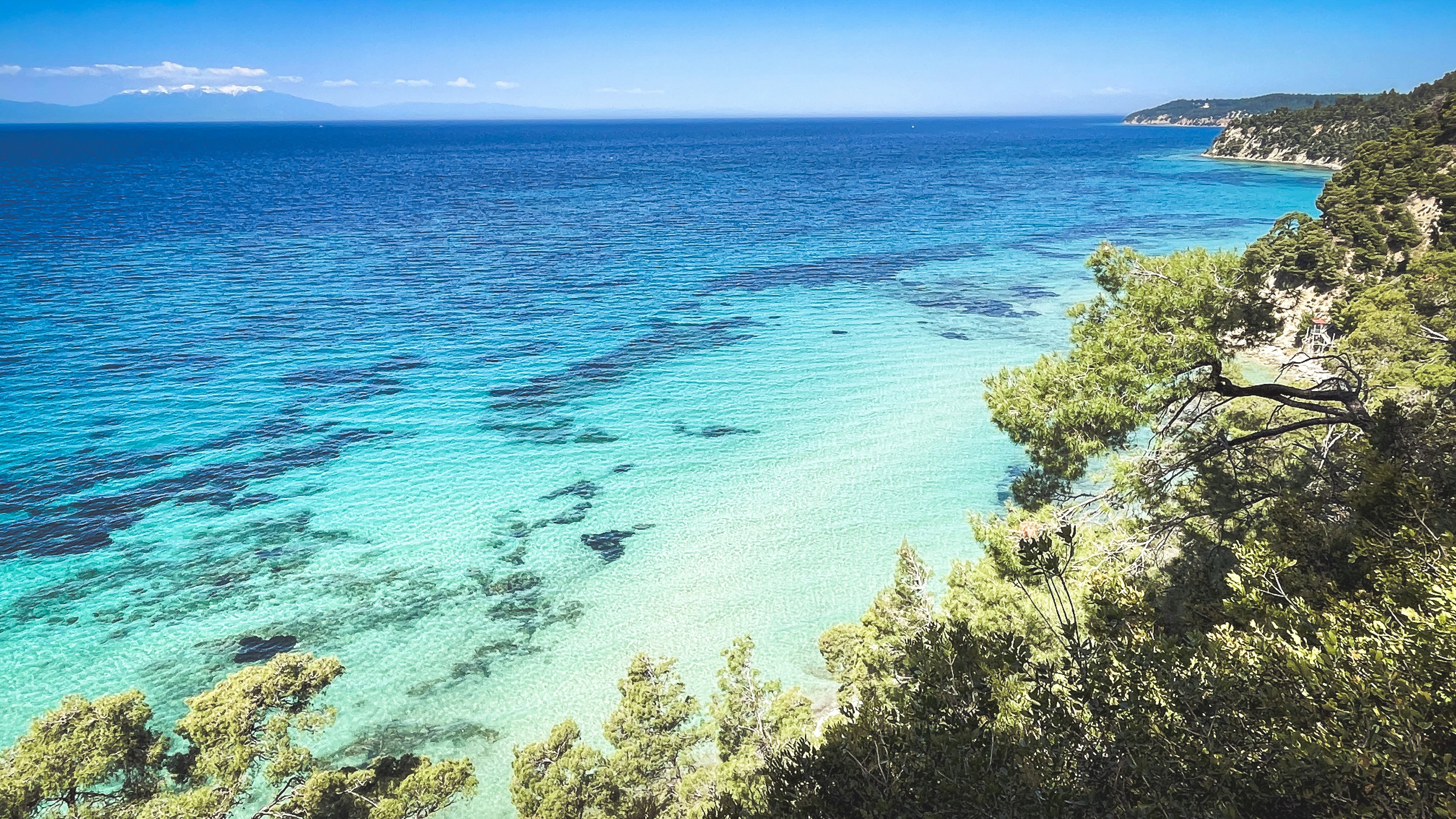 Sunlit Aegean Edge: Coral Waters meet Pine-clad Cliffs