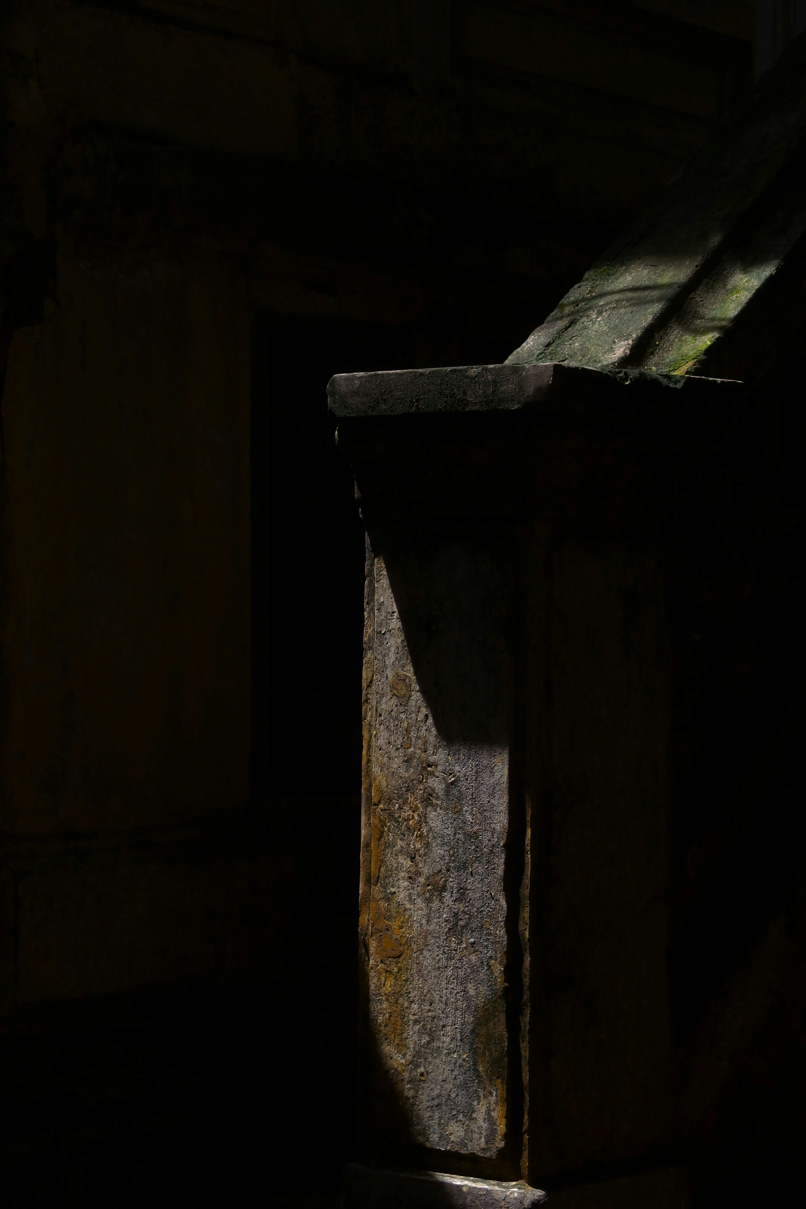 Weathered stone railing catching a sliver of light in a shadowed ruin