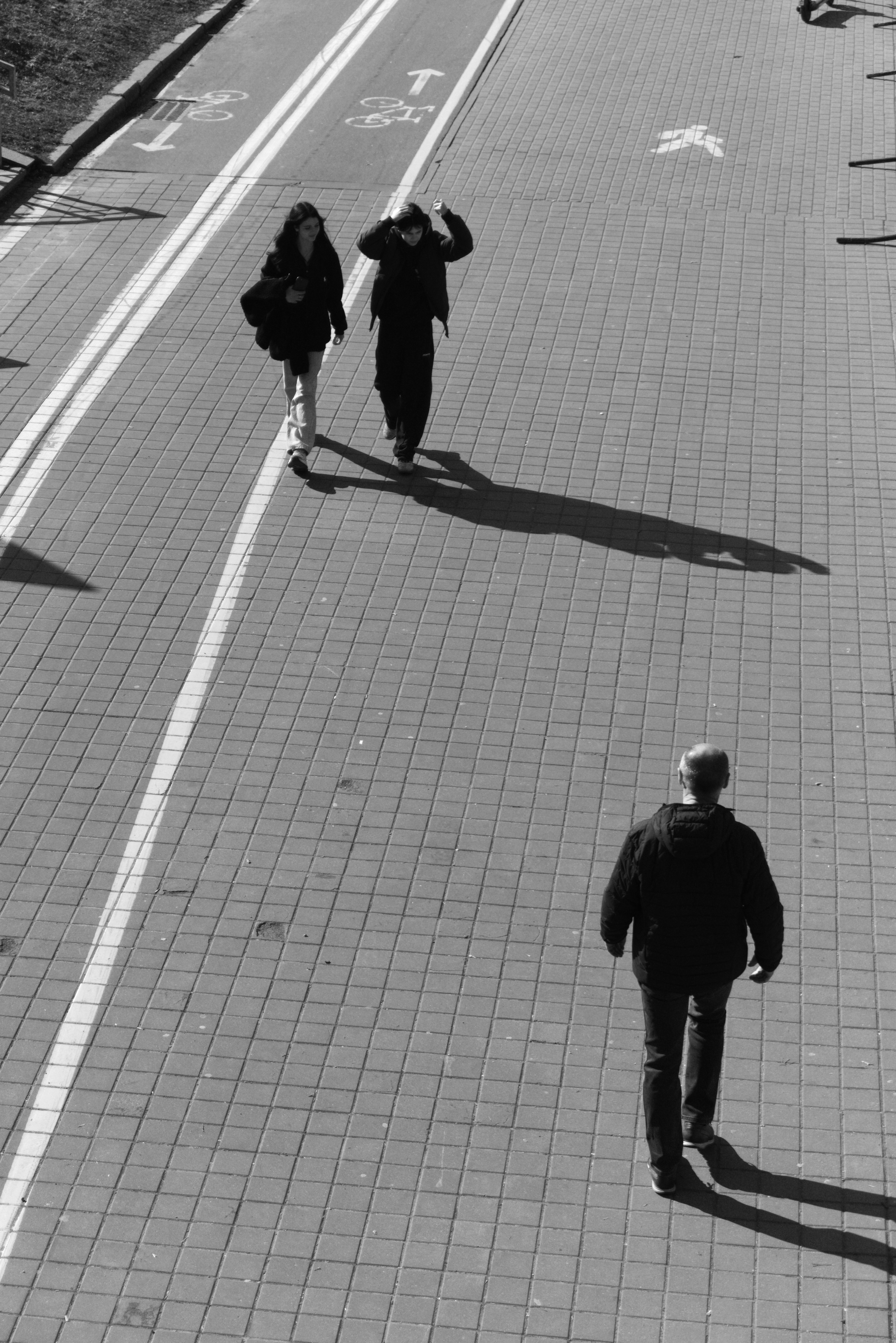 Two pedestrians and a lone passerby on a sunlit grid plaza