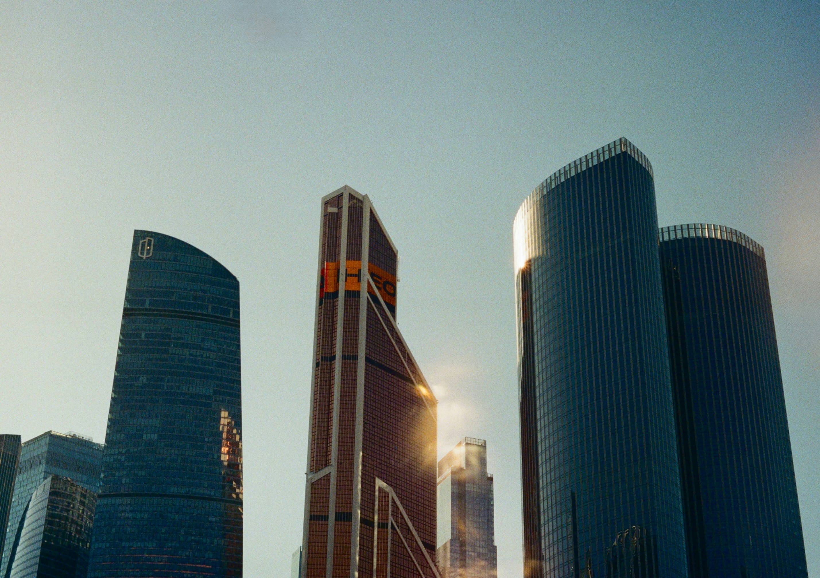 City skyline with tall glass towers reaching toward a pale sky, sun kissing the edges of the buildings.