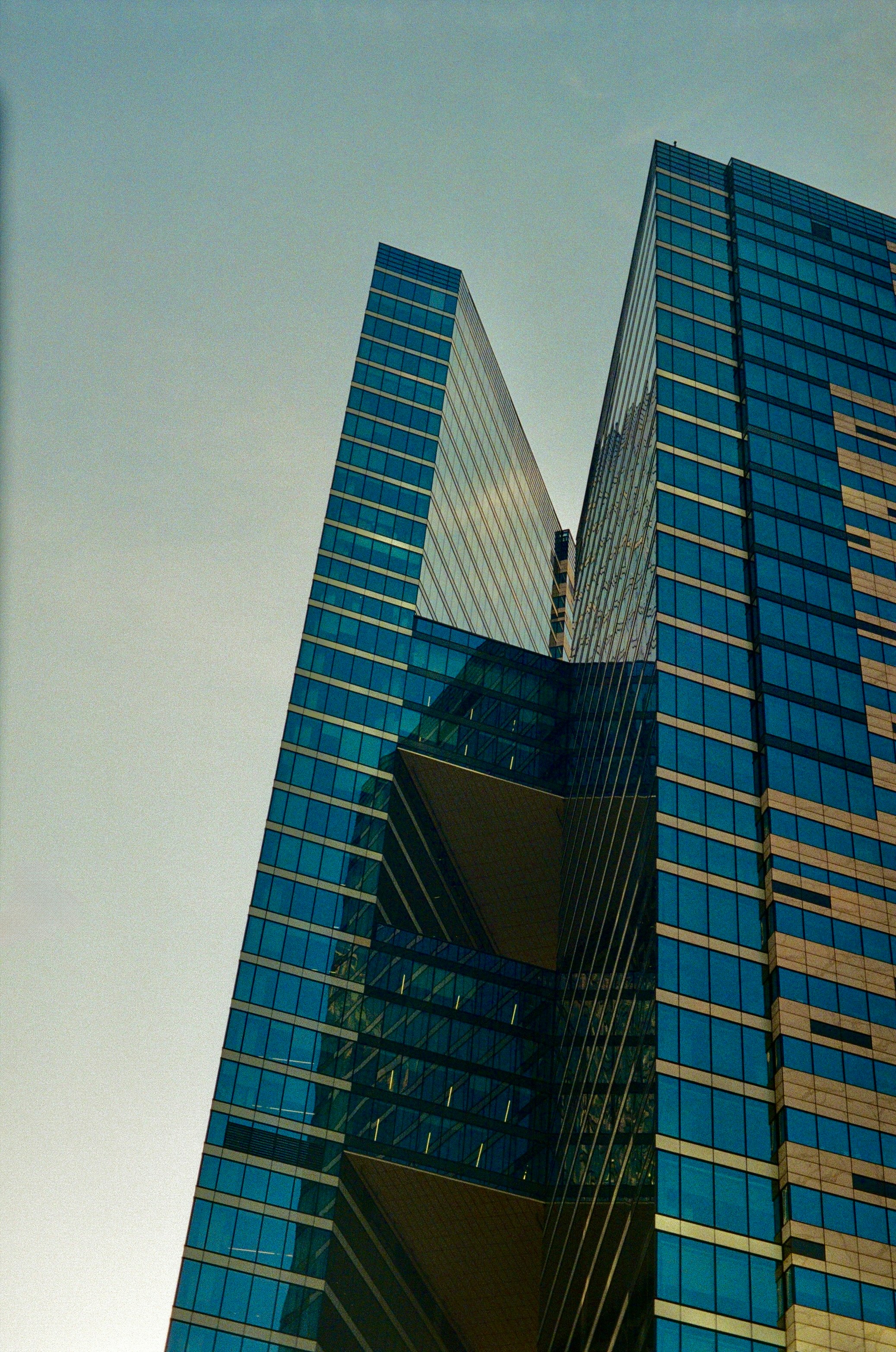 Sleek glass towers slice upward, their mirrored faces reflecting a pale sky and creating a dramatic geometric composition.