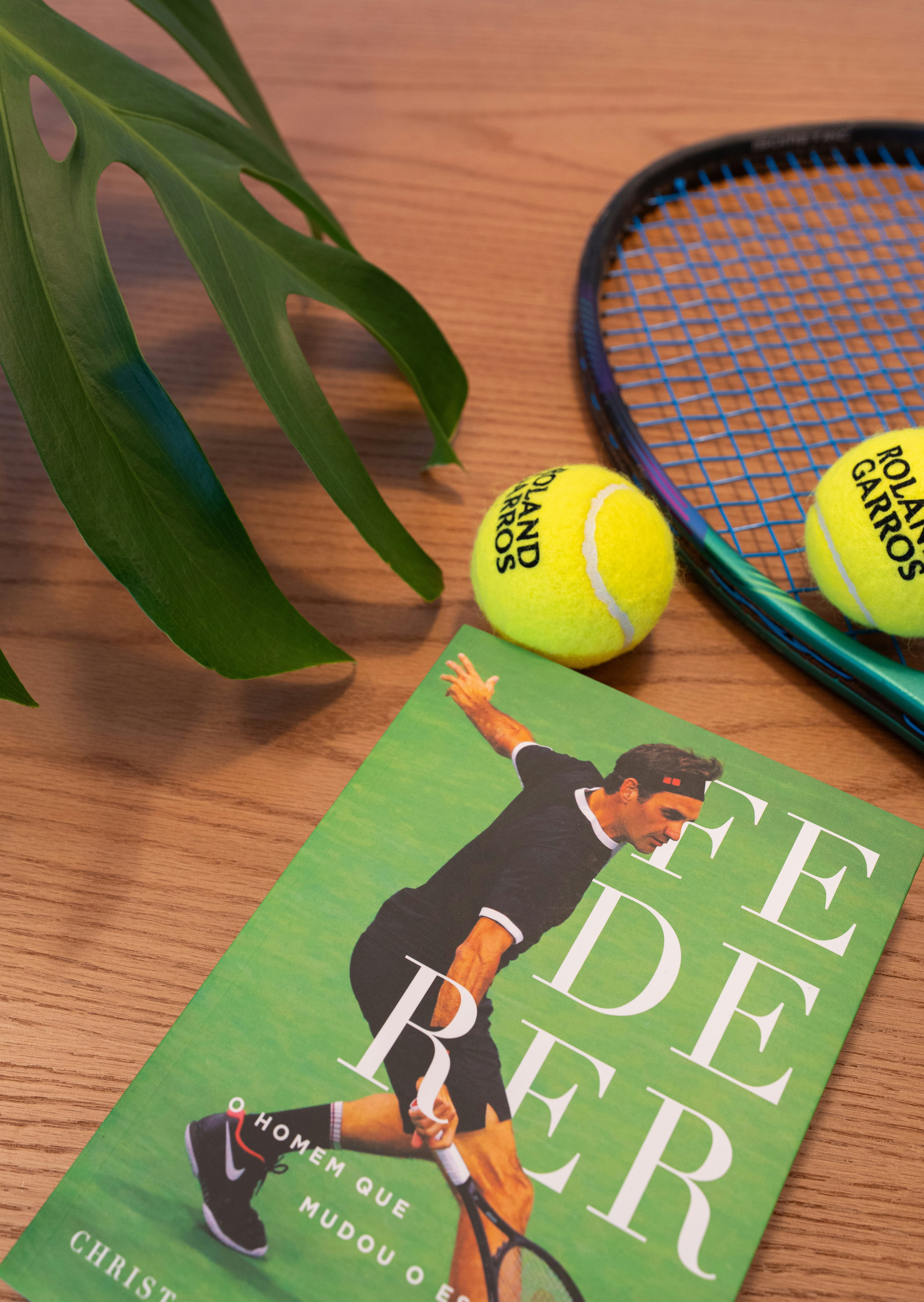 Tennis balls, a racket, and a green magazine lie on a wooden surface, creating a flat-lay of sport and lifestyle elements.
