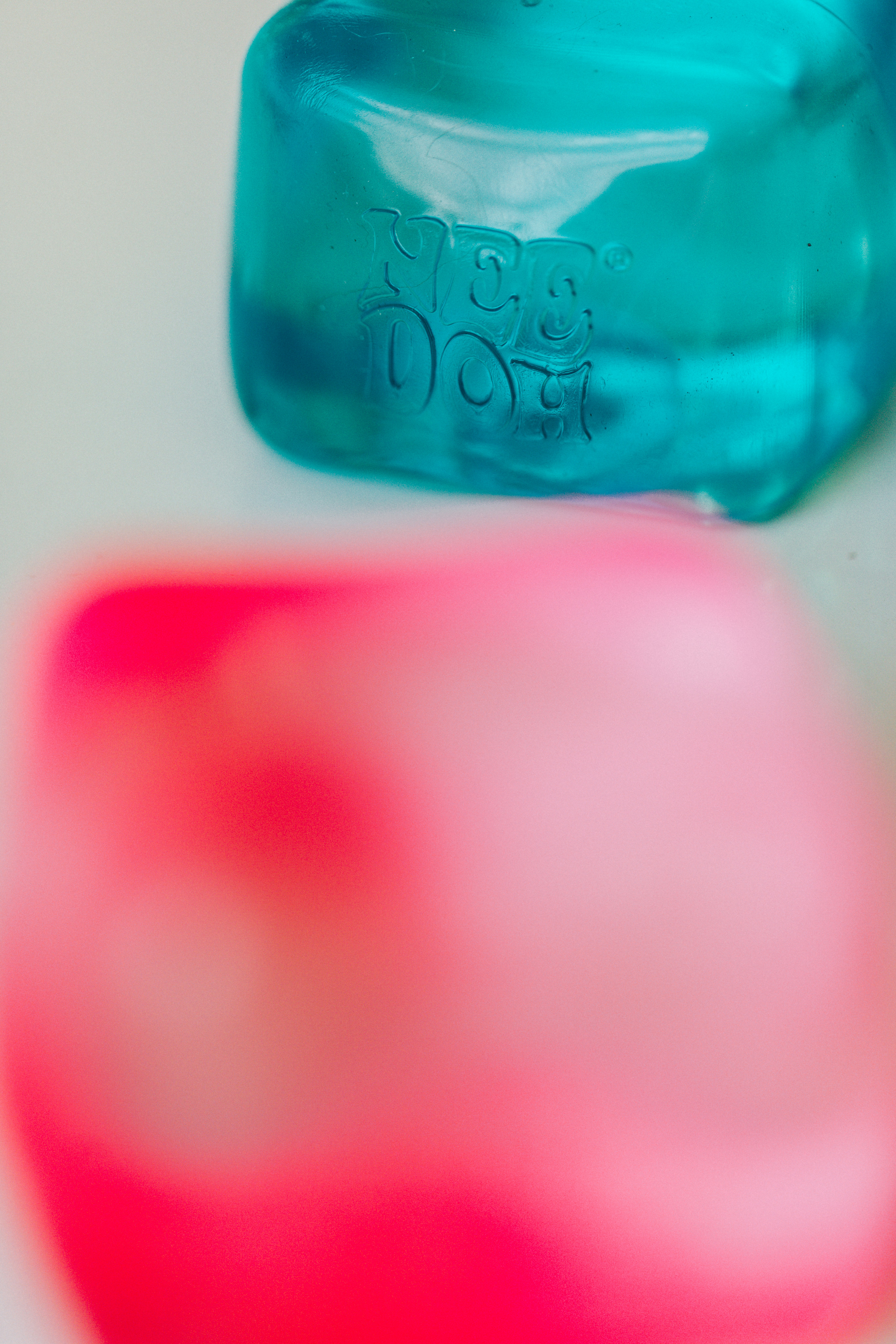 Two translucent gel cubes—turquoise on top and pink below—rest in soft blur, evoking a dreamy still-life composition with an abstract, pastel mood.