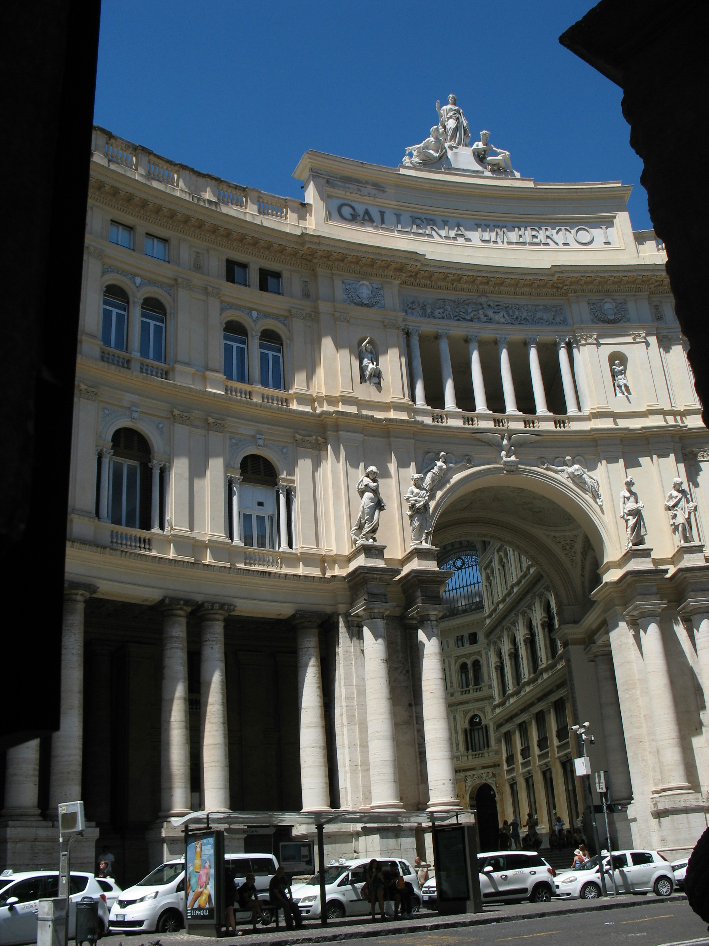 Archway of Grandeur: Traffic, Cars, and Sculpted Facade in Sunlit Piazza