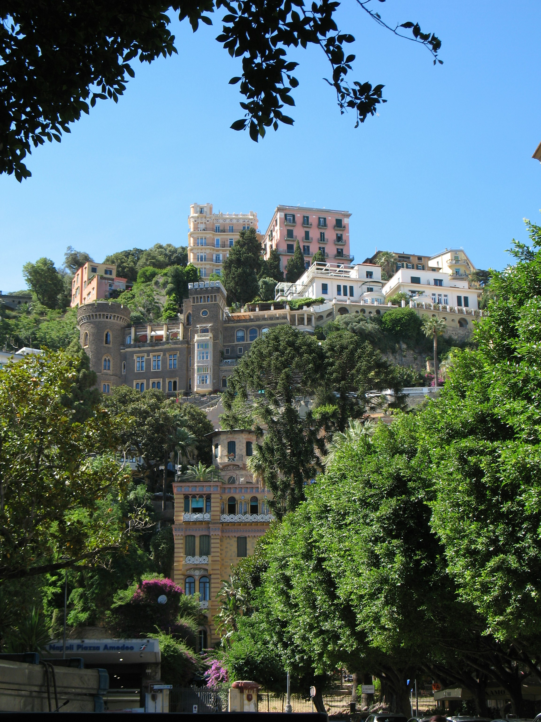 Vibrant hillside village with pastel buildings stacked among greenery under a clear blue sky.