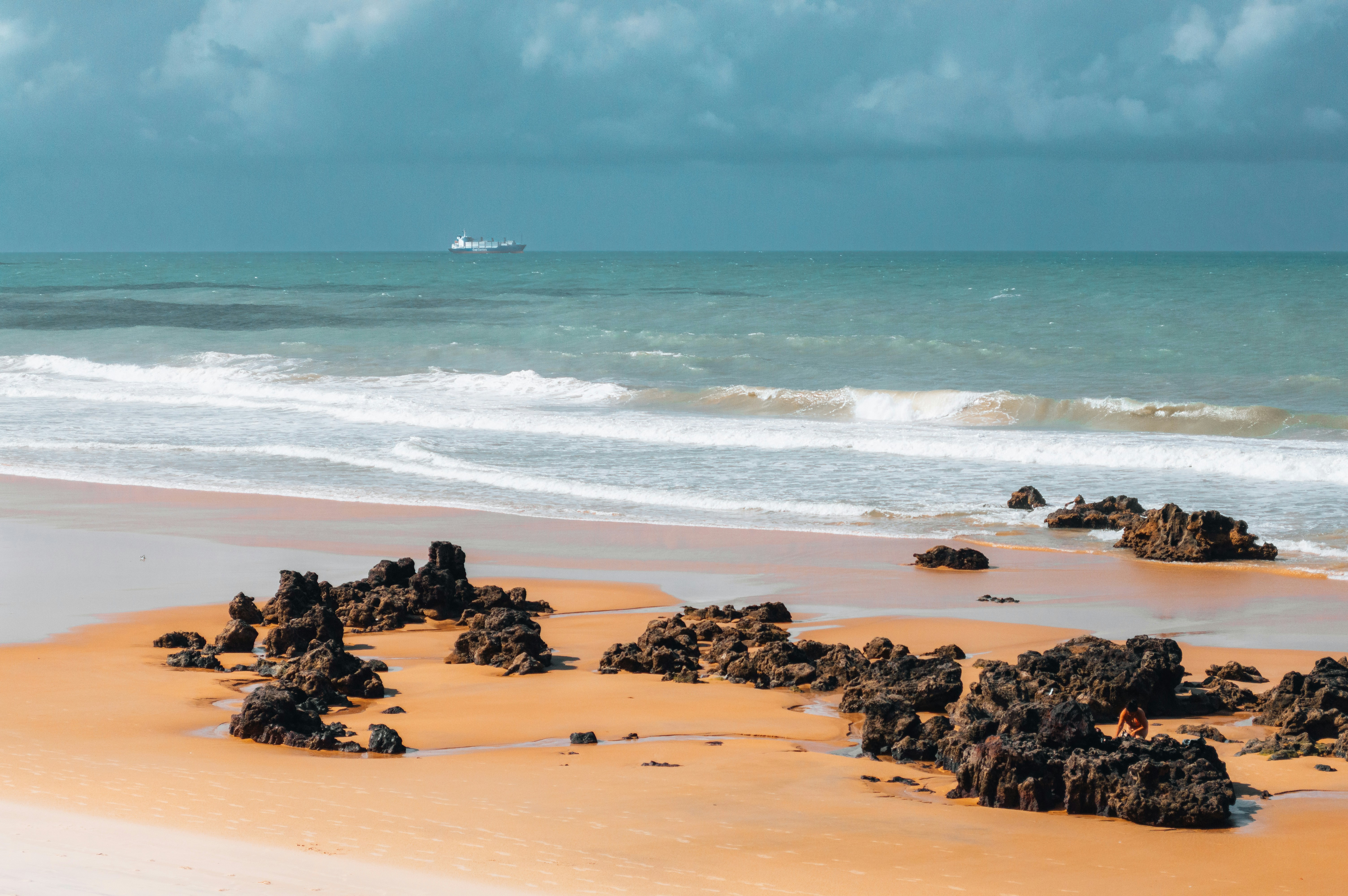Sunlit shoreline and distant boat on a calm turquoise sea