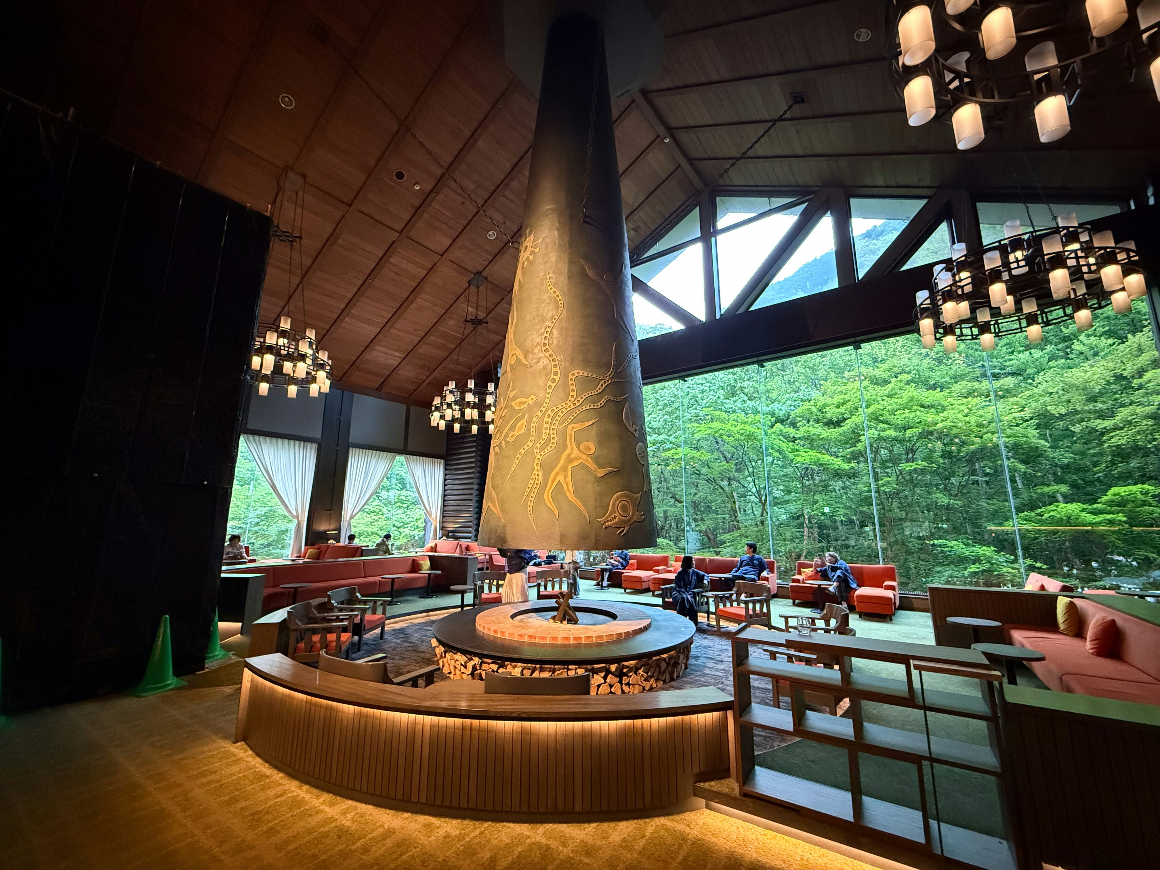 Circular fire pit lounge under dramatic hewn column in glass-walled resort lobby