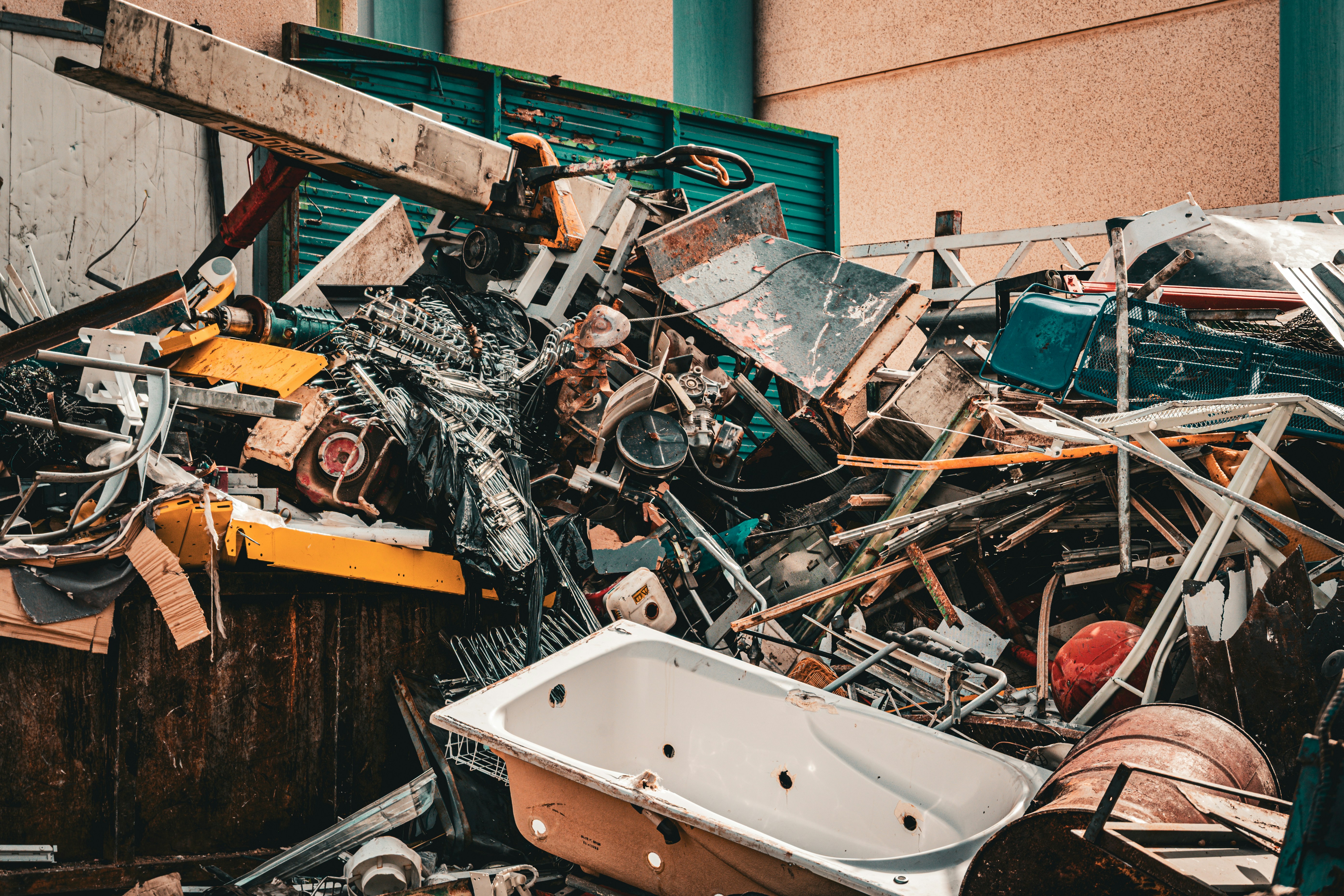 Piled scrap and broken appliances form a chaotic scrapyard scene with metal, plastic, and concrete textures. The composition emphasizes tangled debris and a stark industrial clutter motif.
