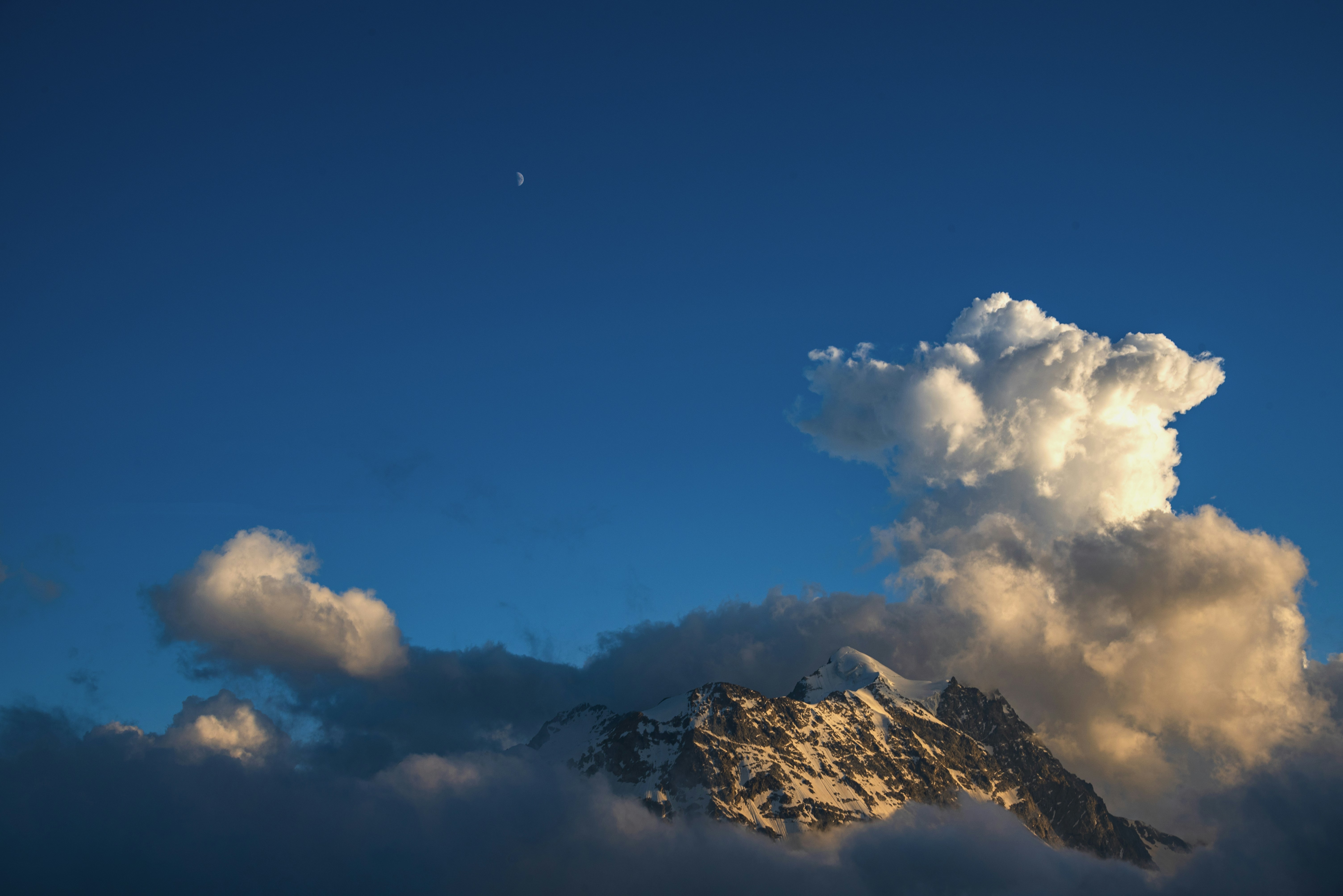 Luminous Peak Emerging Through Cloudscape Under a Crescent Moon