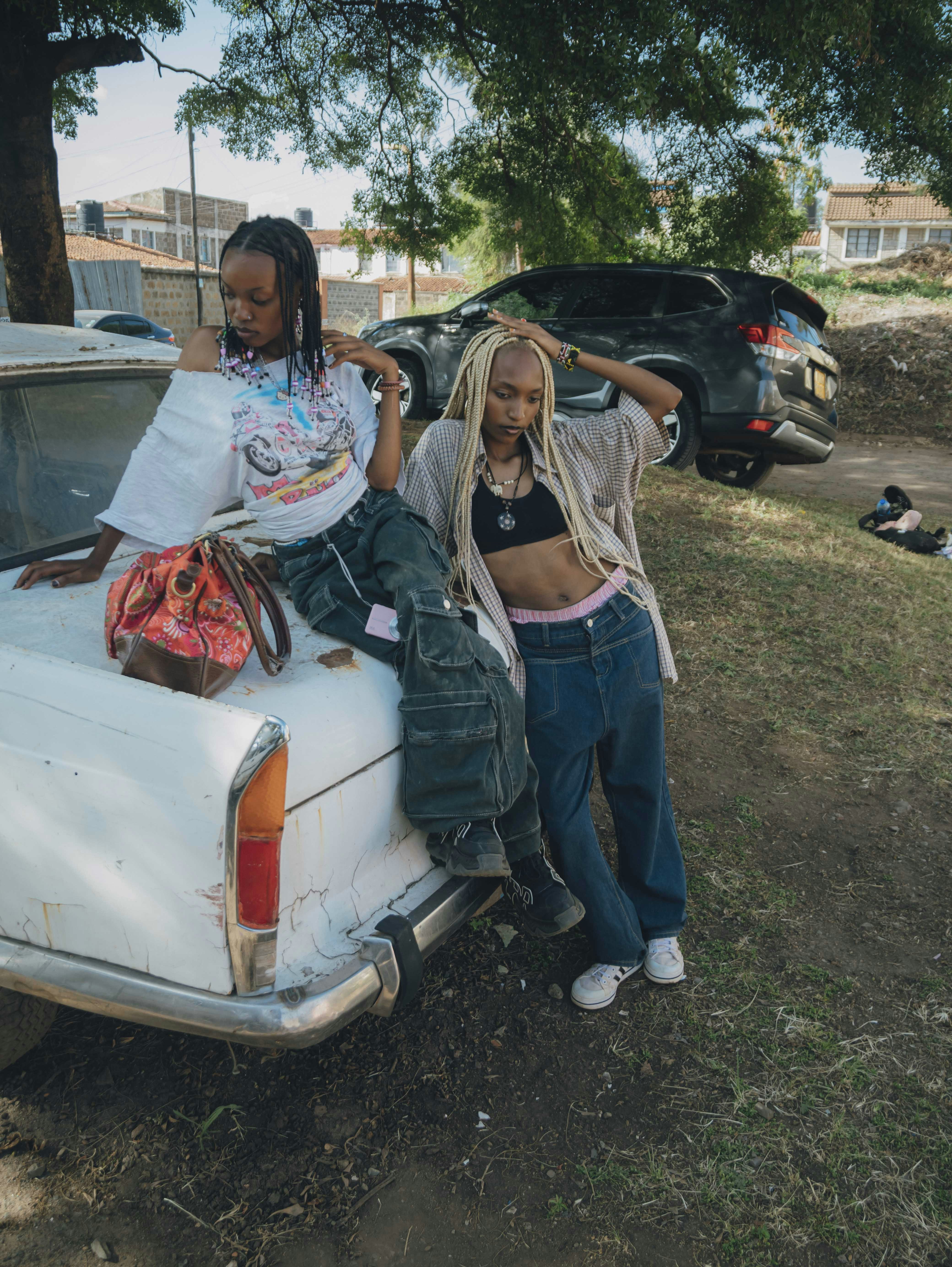 Two friends posing on a sunlit vintage truck bed beside a cluttered lot