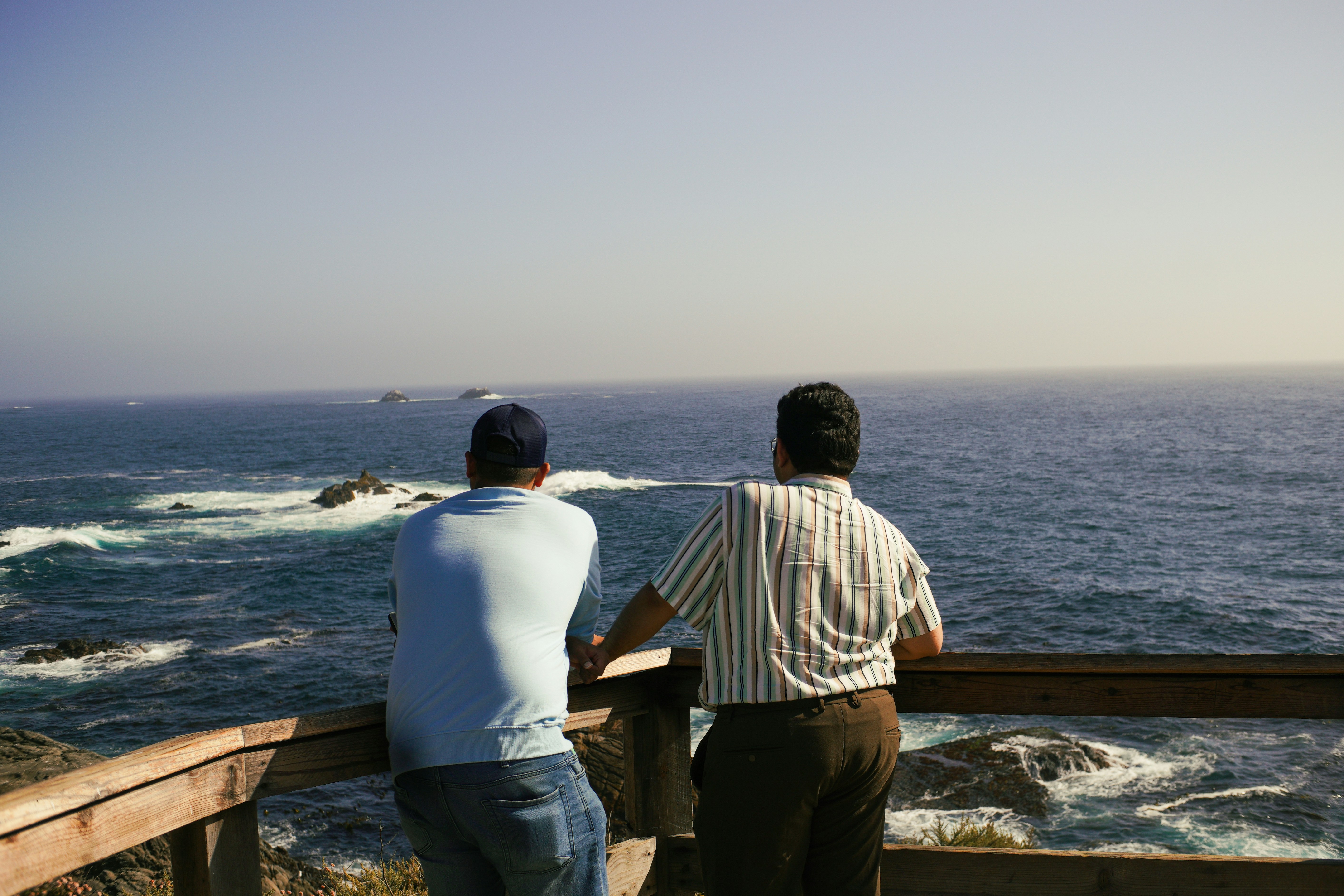 Two viewers on a coastal overlook watch the sea and distant rocks