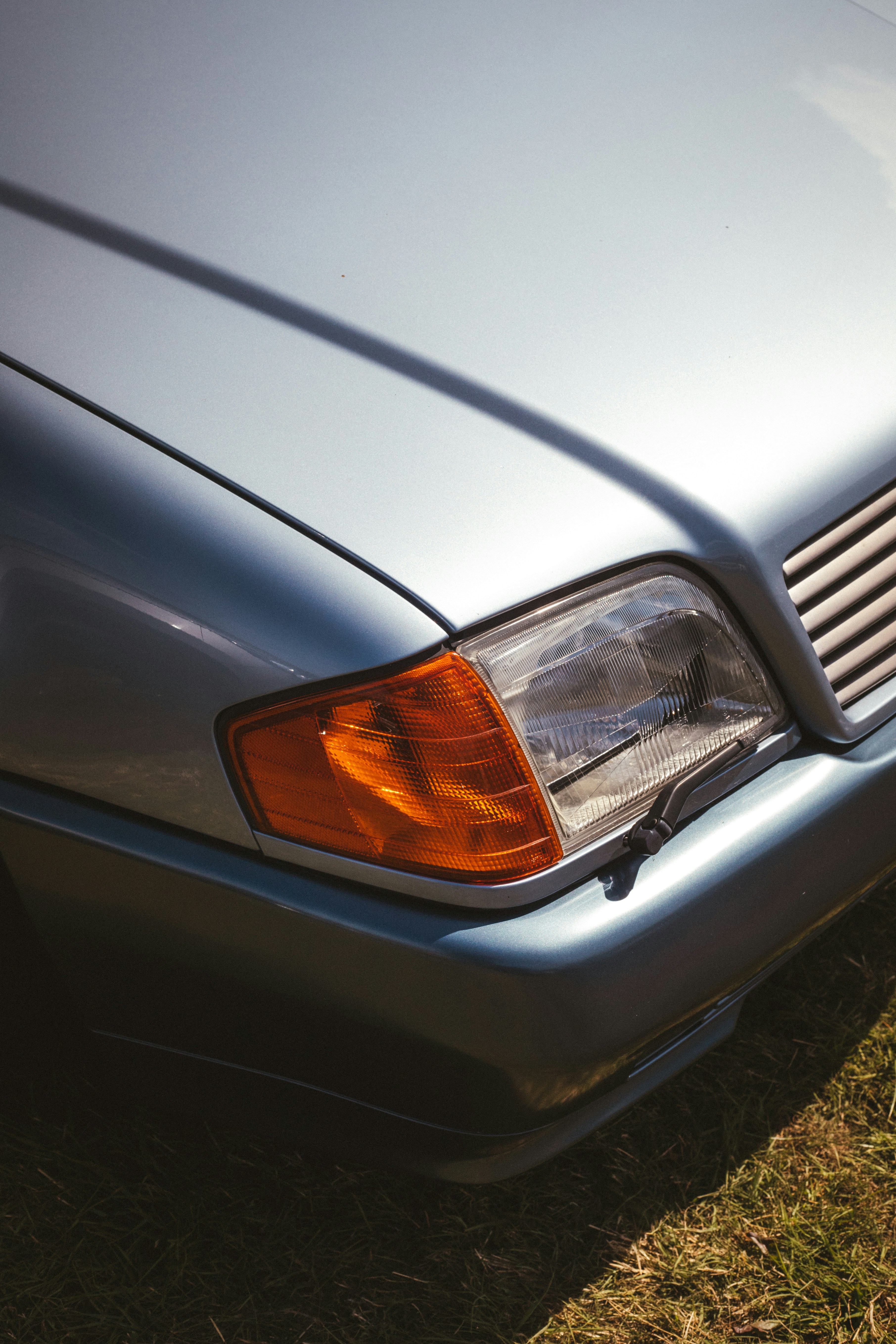 Close-Up of an Old Blue Car Headlight and Hood in Sunlit Grass