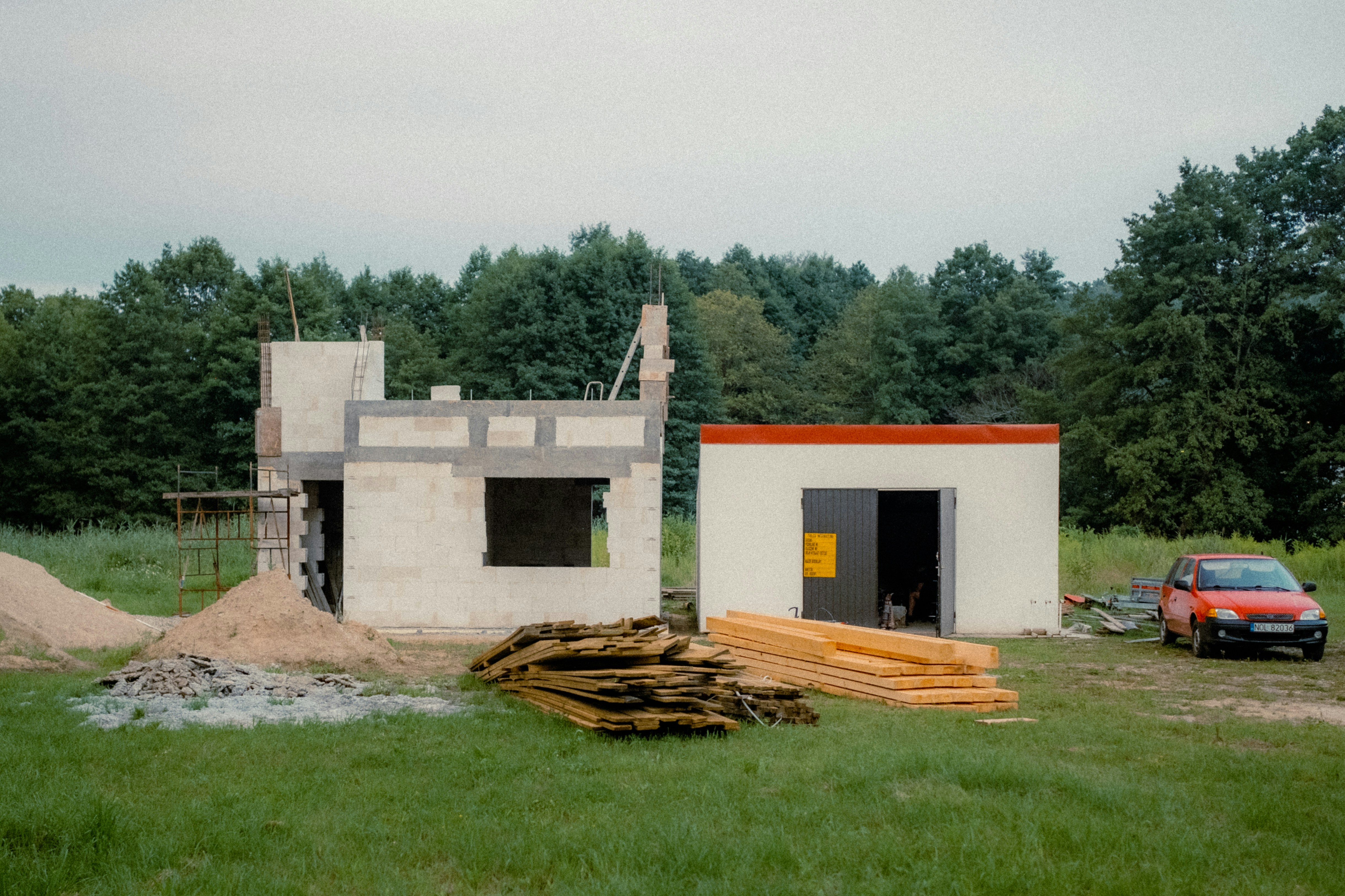 Construction Site Dreams: A Halfbuilt Structure Meets a Quiet Car on the Perimeter