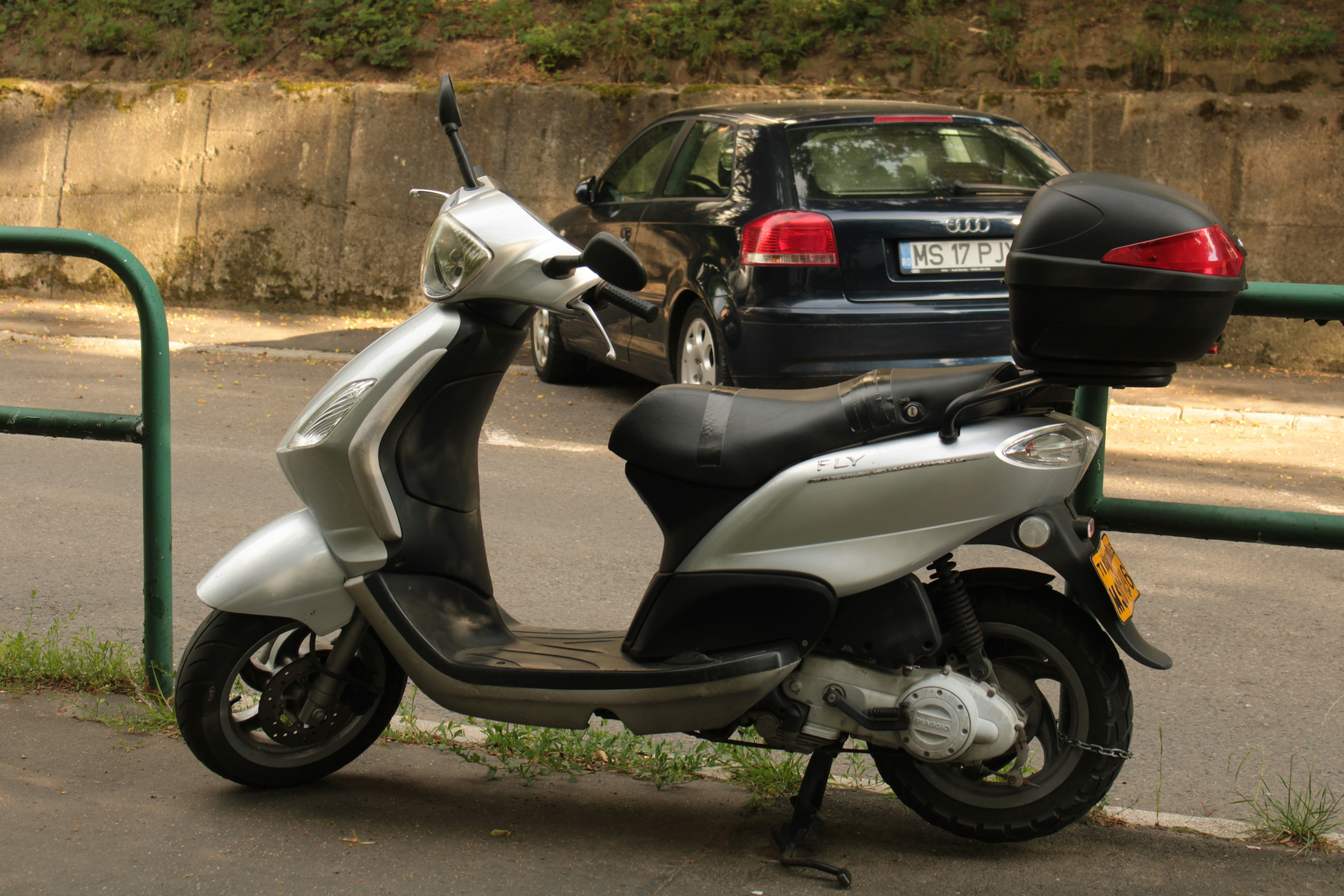 Silver scooter with rear top box parked along a road