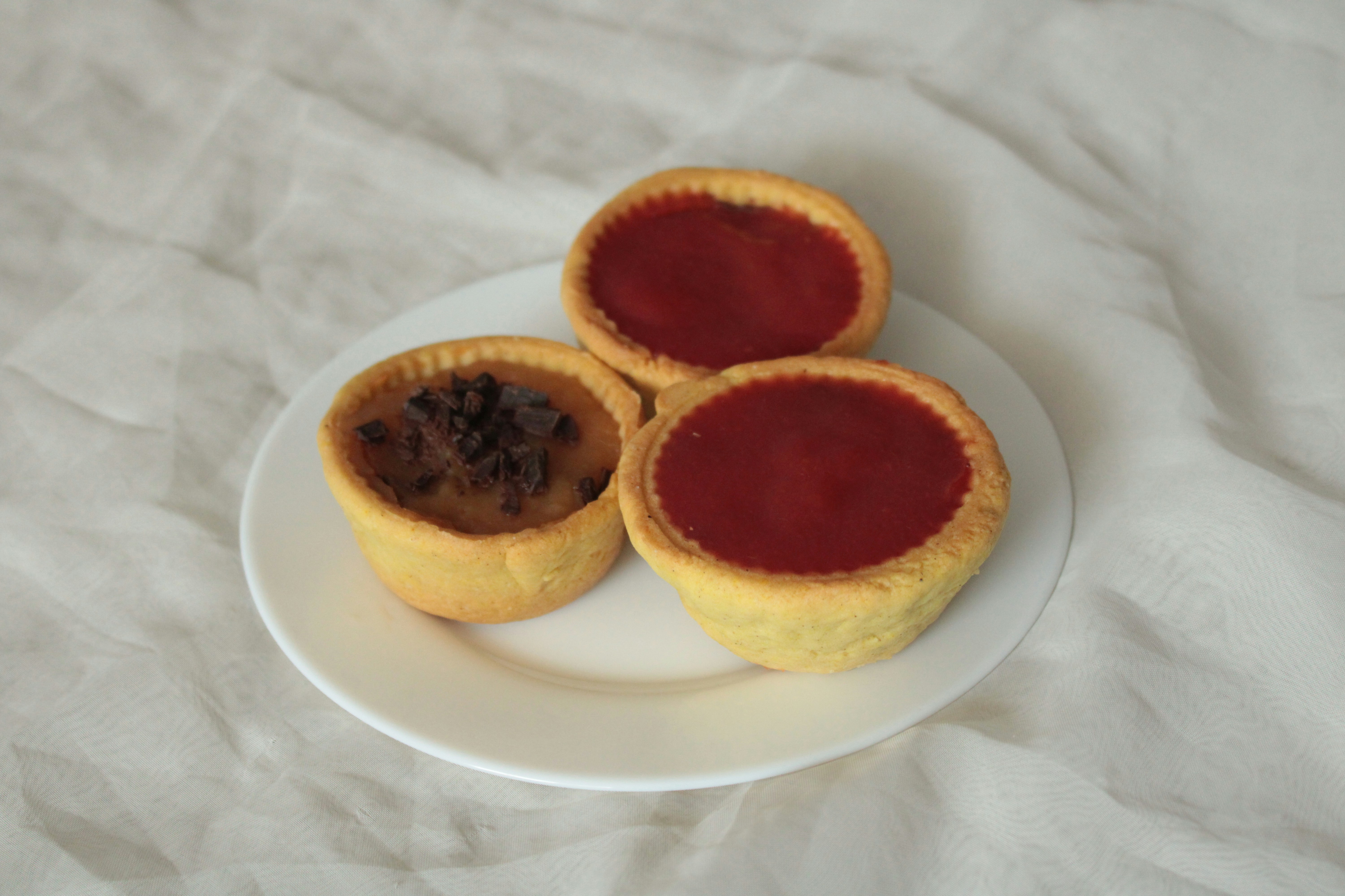 Three Tartlets on a White Plate: Red Gel, Dark Filling, Soft Pastry