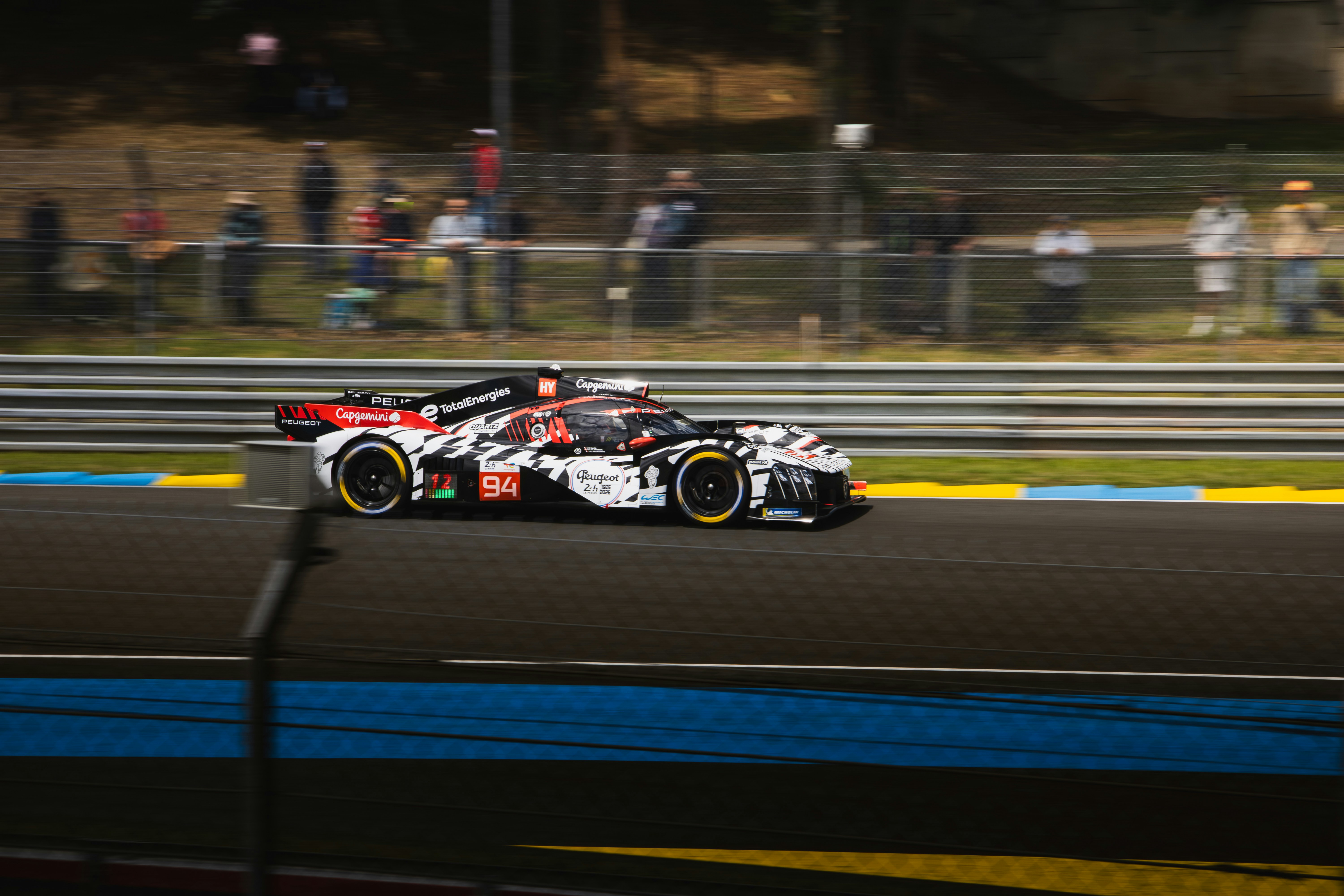 Red-and-White Racecar Races Past Blue and Yellow Barriers Under Night Lights