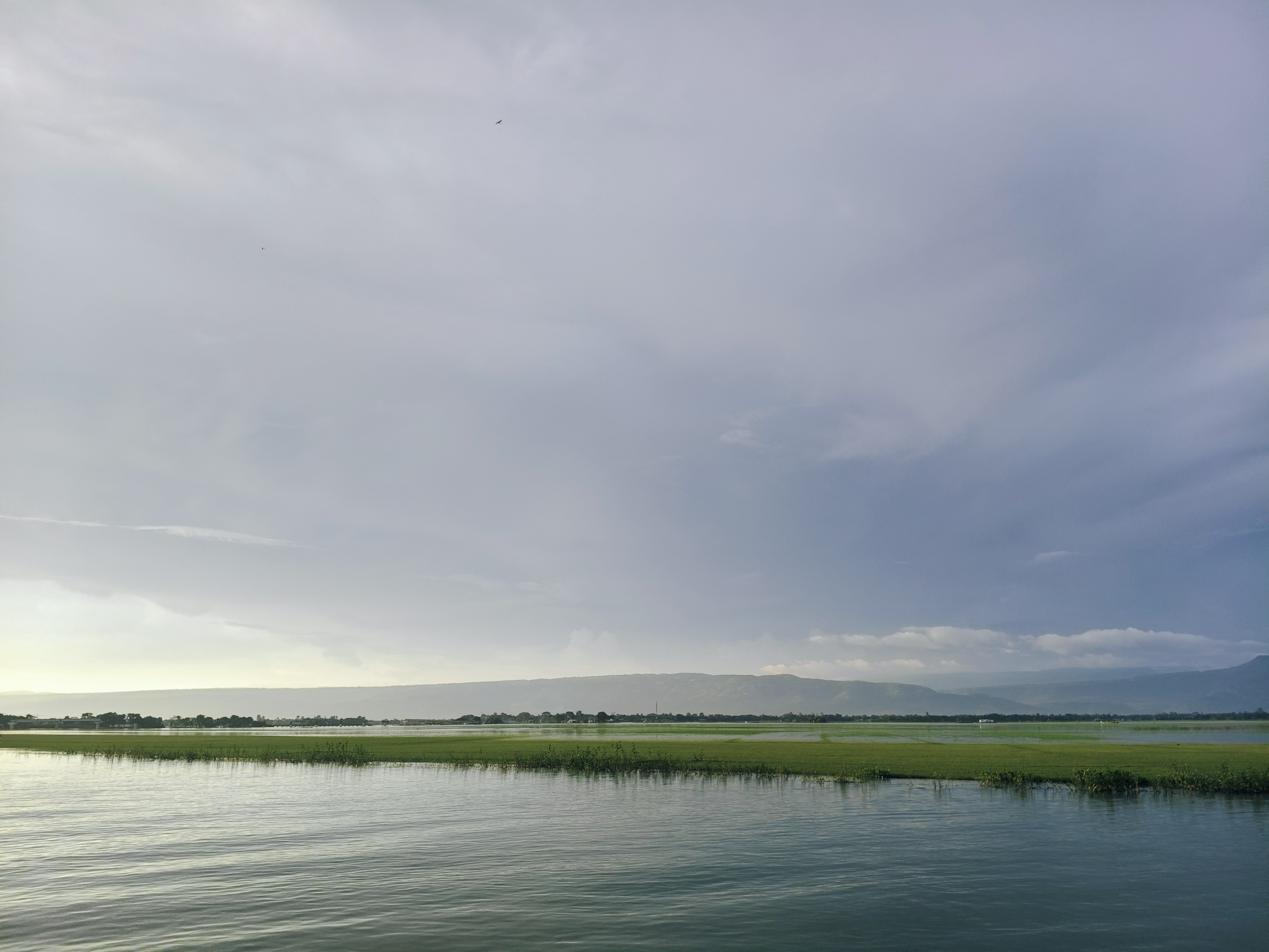 A dramatic sky stretches over tranquil wetlands as distant hills fade into the horizon, capturing nature's calm before the rain.