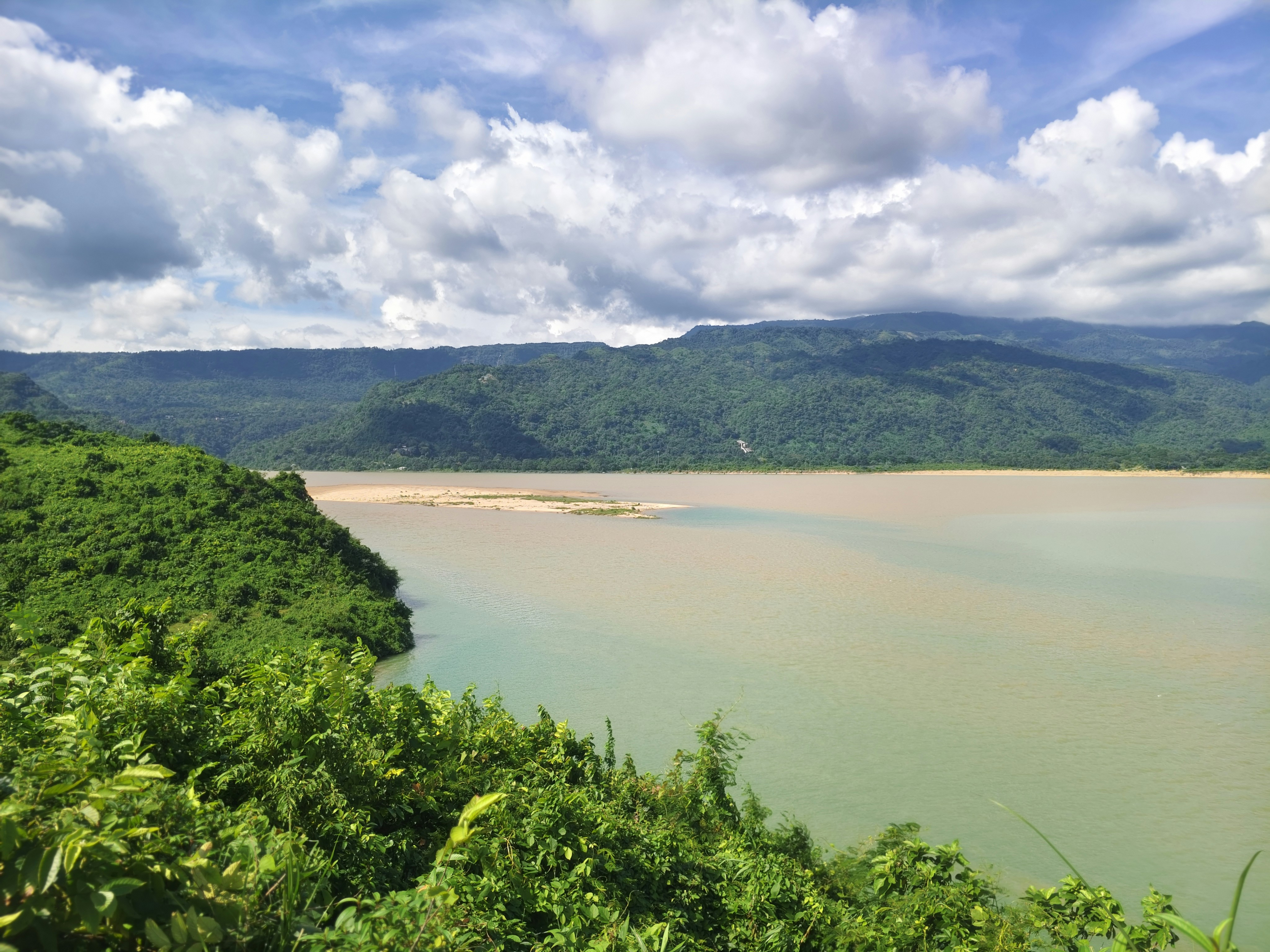 A winding river flows between lush green hills beneath dramatic clouds, revealing the untouched beauty of the countryside.