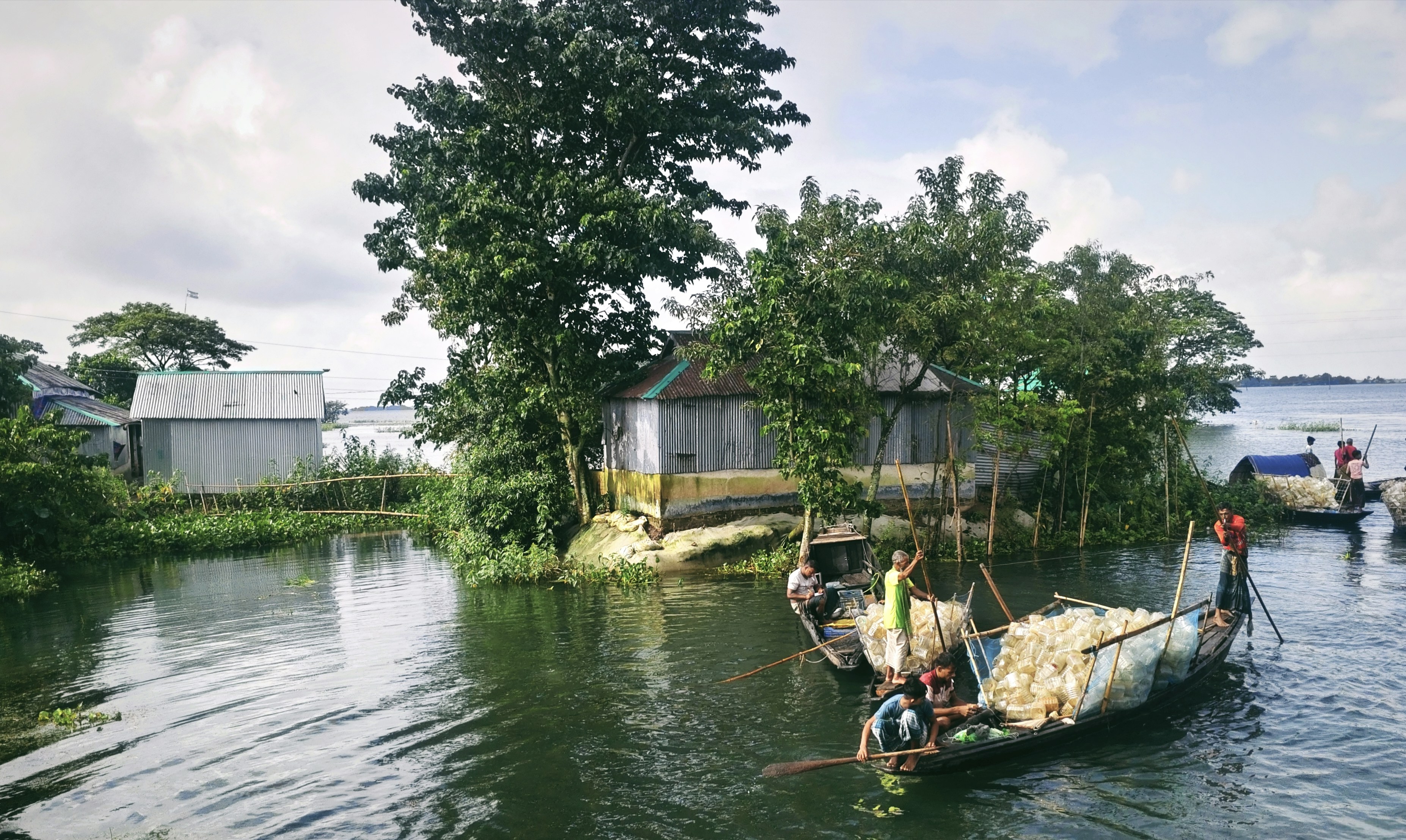 Daily life unfolds on a quiet riverside as wooden boats, village homes, and calm waters tell a timeless story.