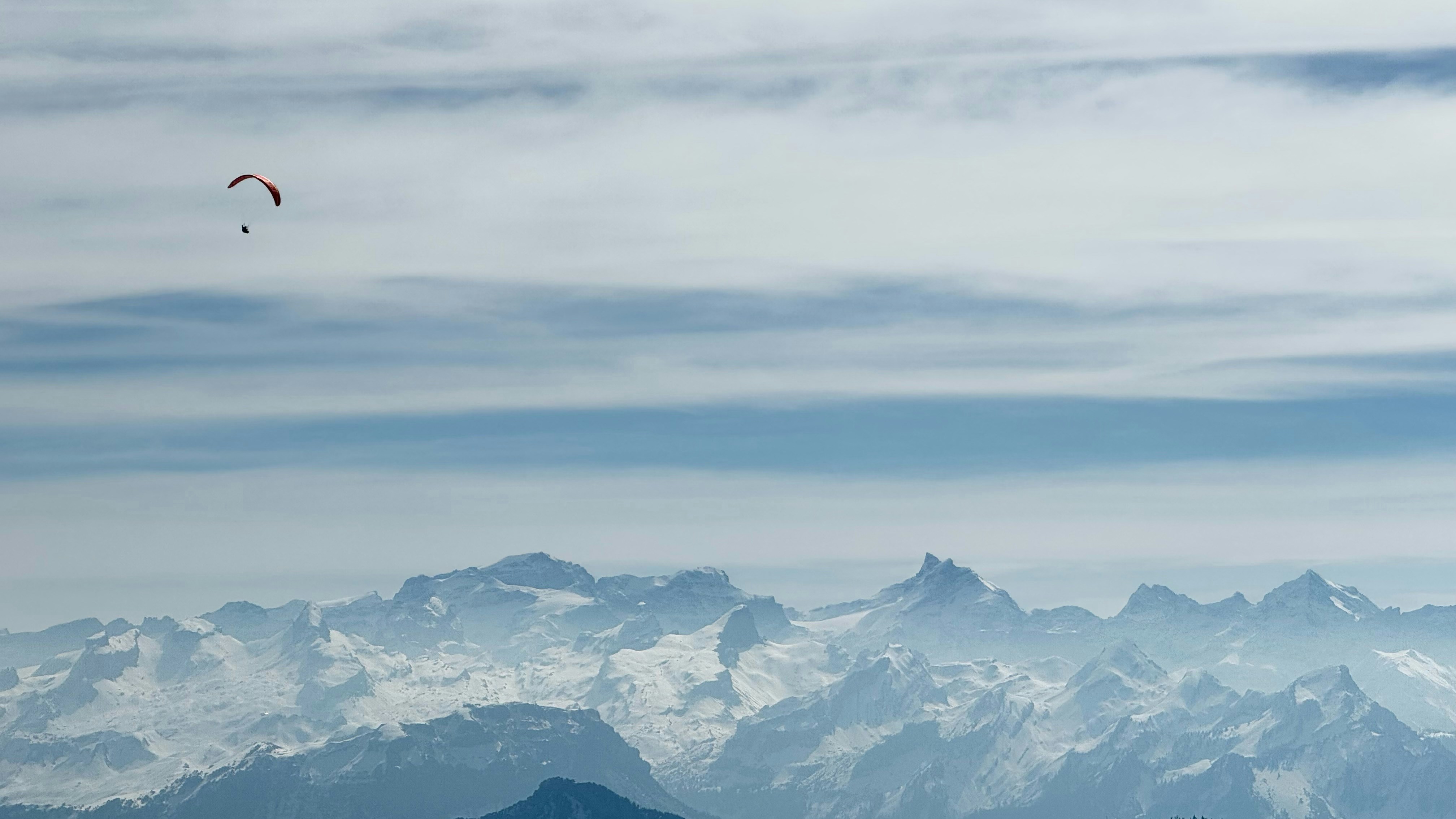 Alpine Glide: A Solo Paraglider Above a Snow-Capped Range