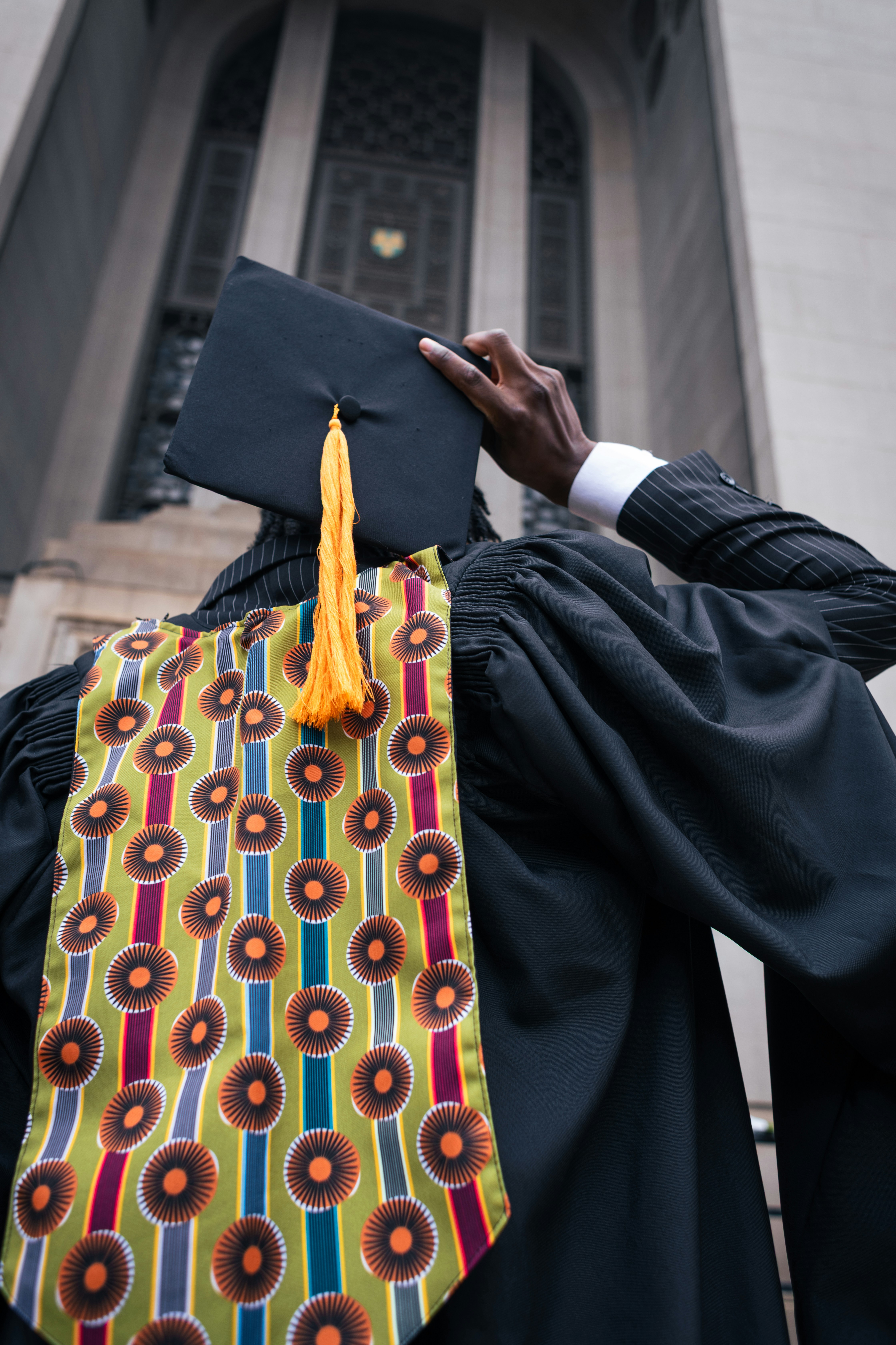 Graduate in cap and gown tilts cap toward cathedral steps, colorful sash flowing down the back. The scene emphasizes achievement and ceremony without extraneous details.