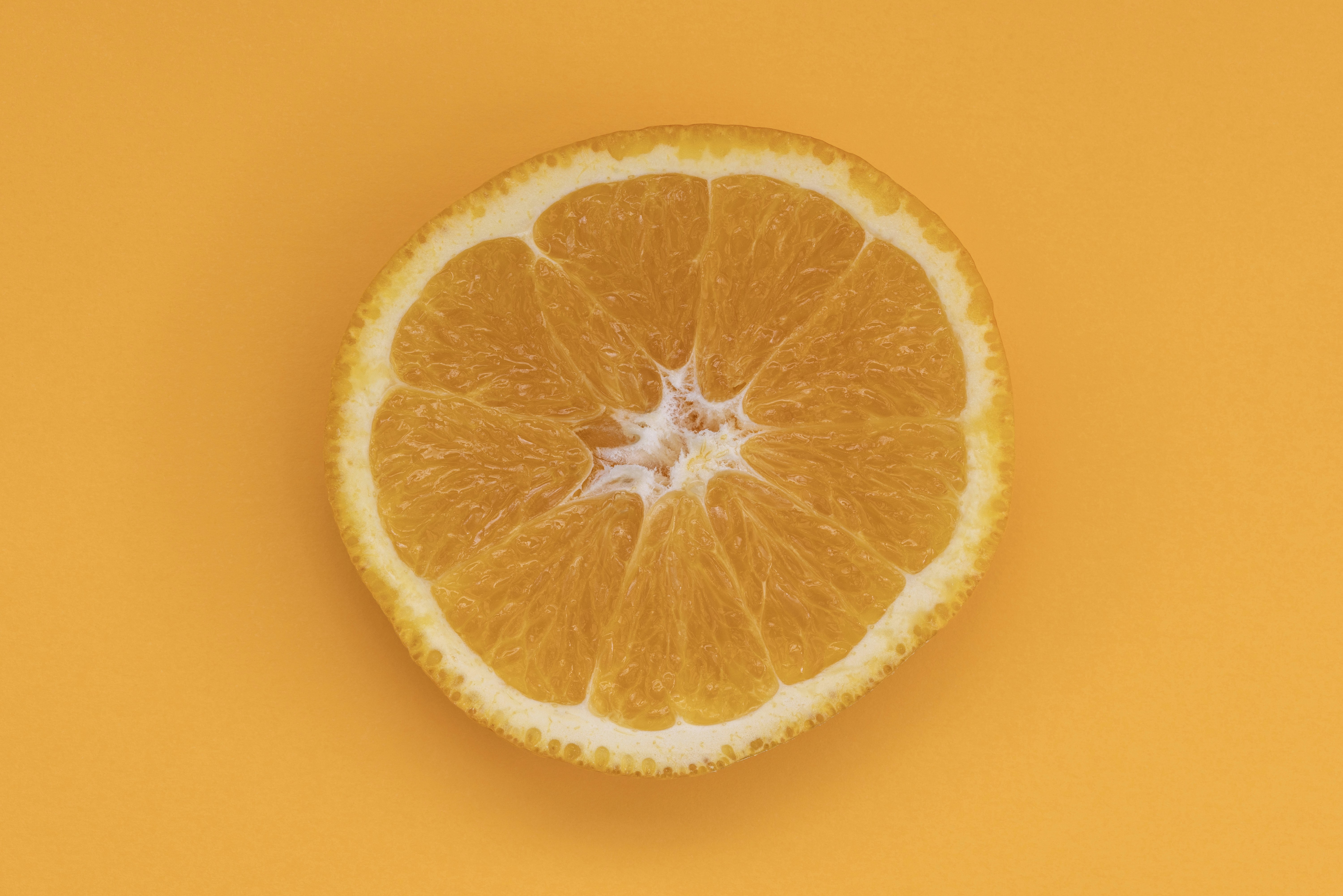 Bright orange cross-section centered on a warm amber backdrop, highlighting the citrus texture and juicy segments. Logo-free, minimal composition with a clean, flat background.