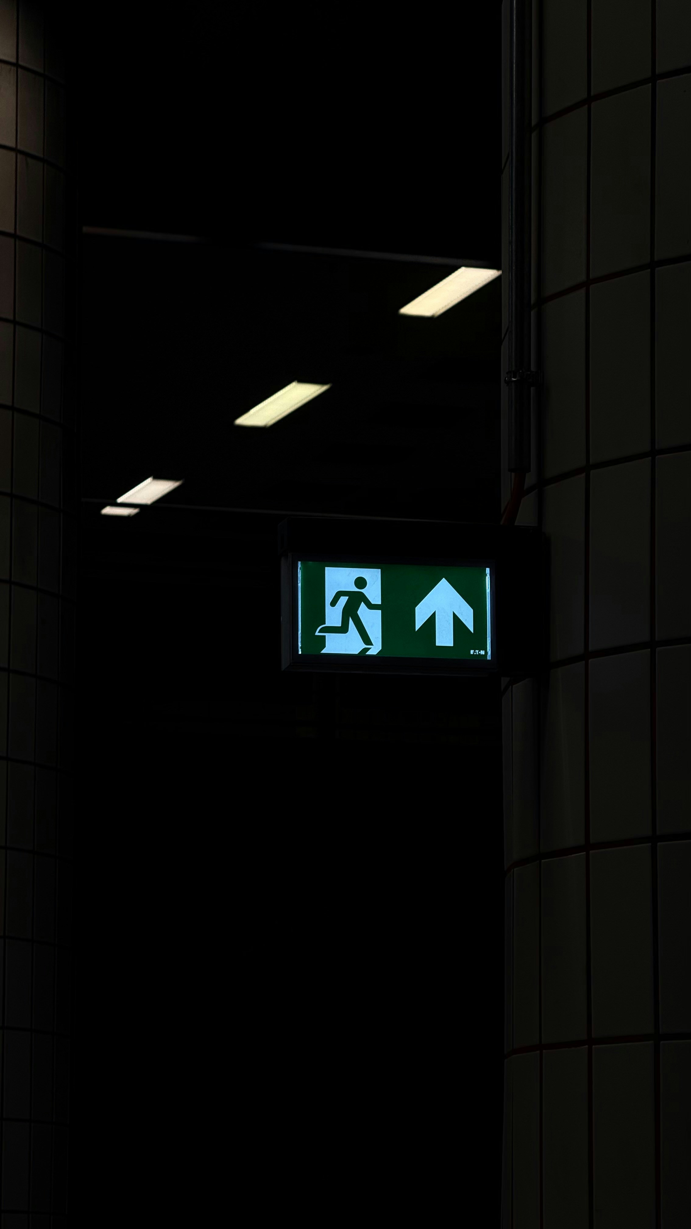 Emergency Glow: A Green Exit Sign Amid Dim Tile Corridors