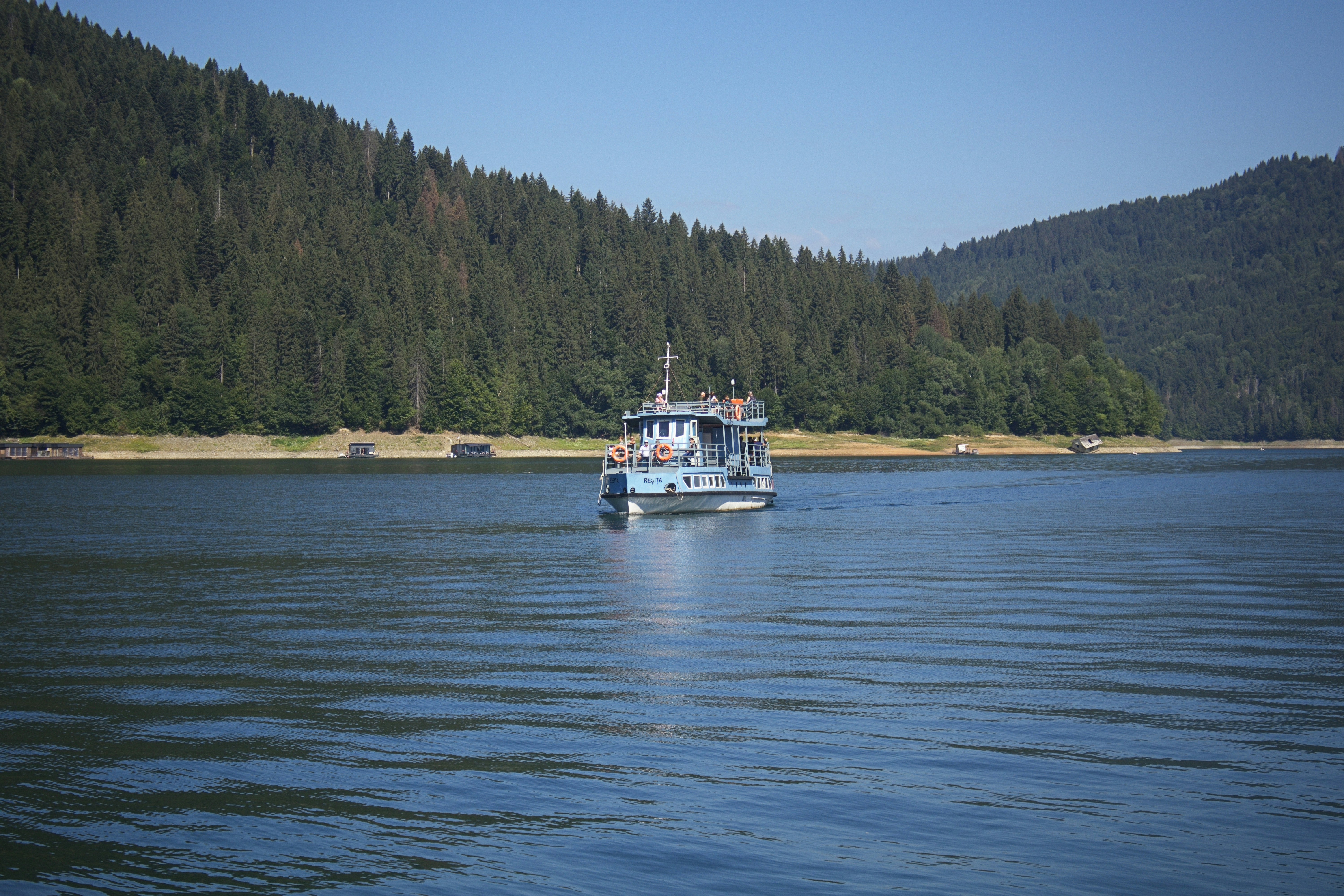 Blue-White Boat Cutting Through Calm Waters Toward a Timbered Shore
