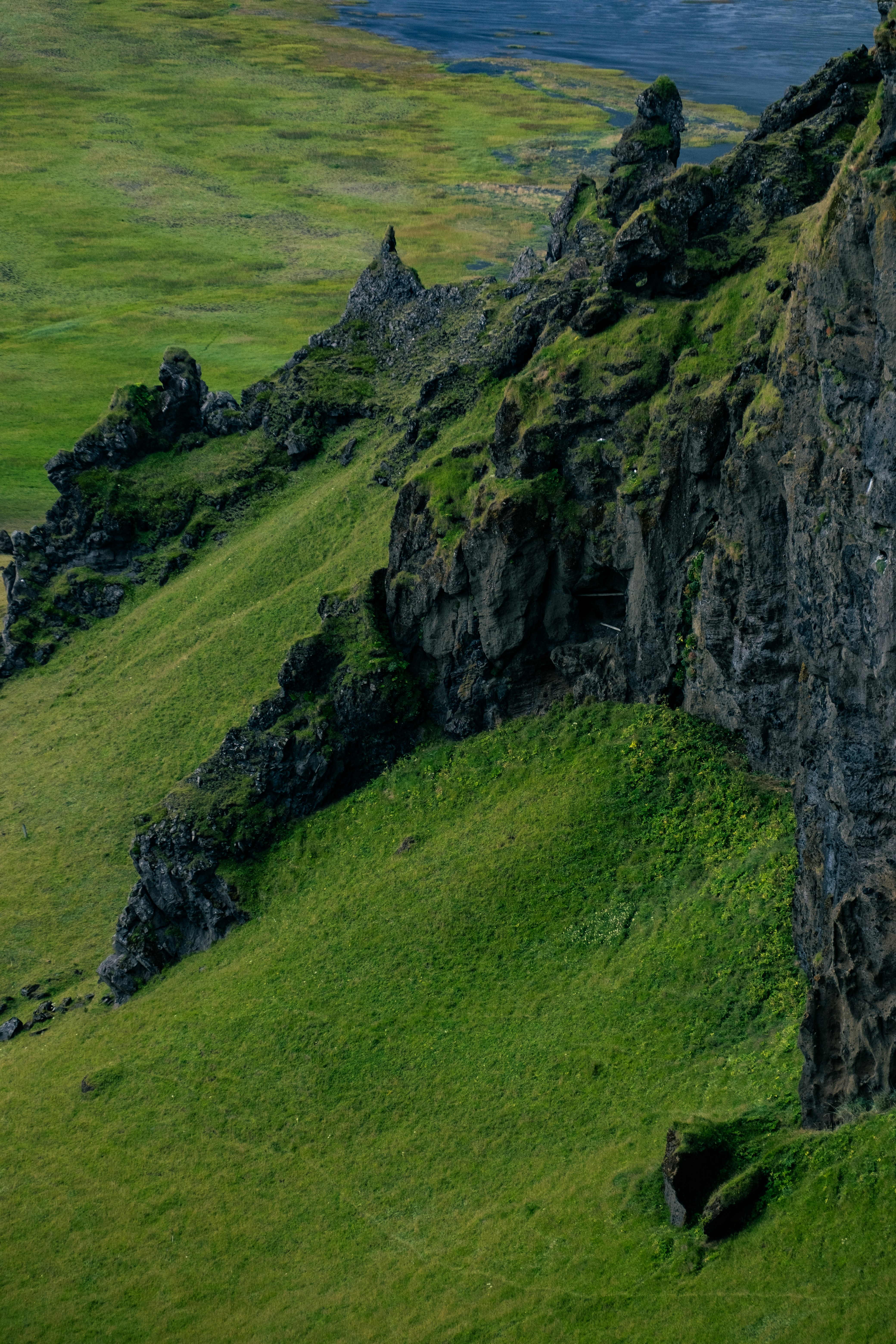 Lush green slopes rise along a rugged rocky ridge by the coast, with steep cliffs and a mossy terrain accenting the dramatic landscape.