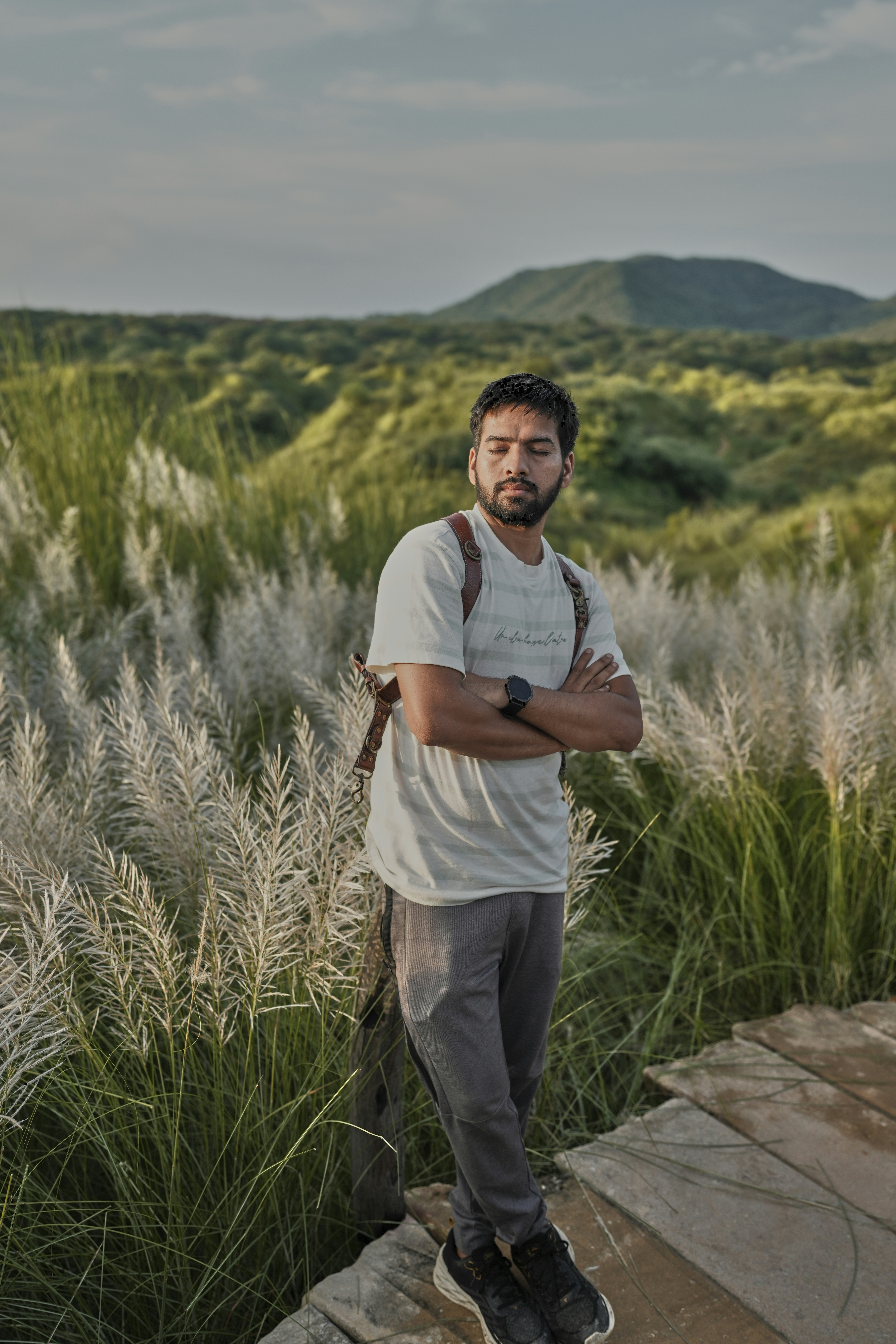 Crossed arms, quiet resolve: a man stands among tall grasses at sunset