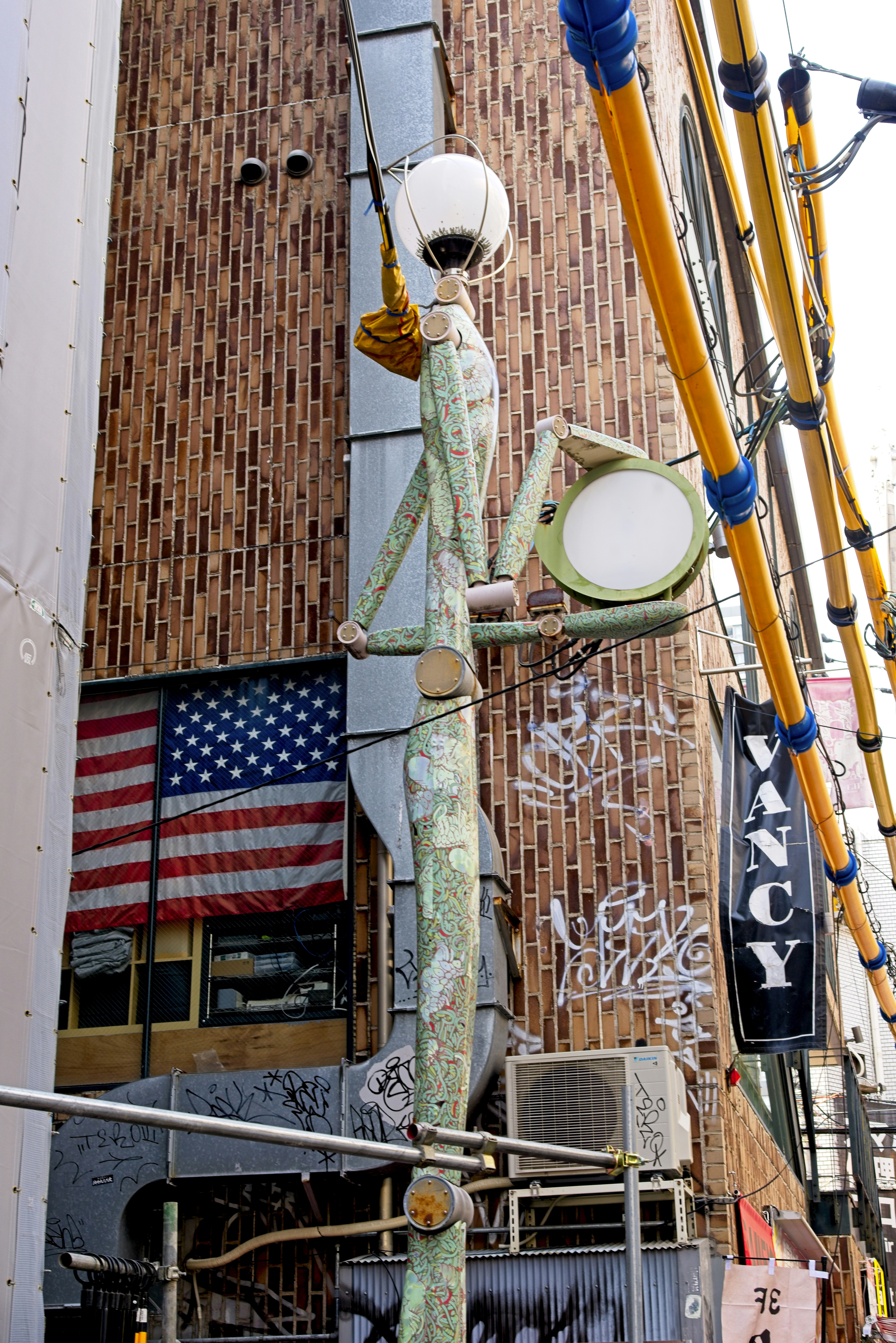 Urban Neon and Rust: A Leaning Sculpture Amid Brick and Neon