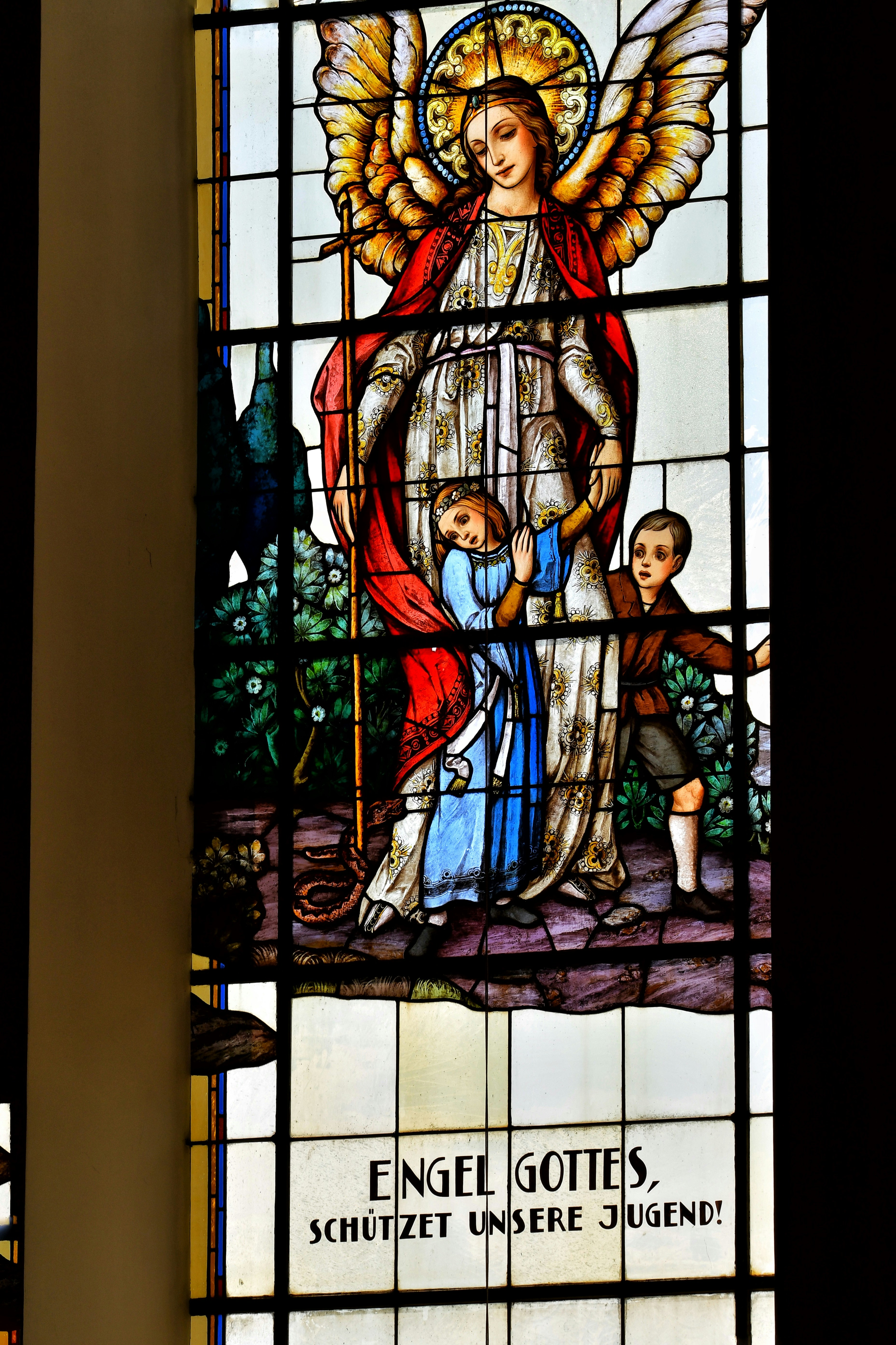 Stained glass window showing an angel protecting two children.