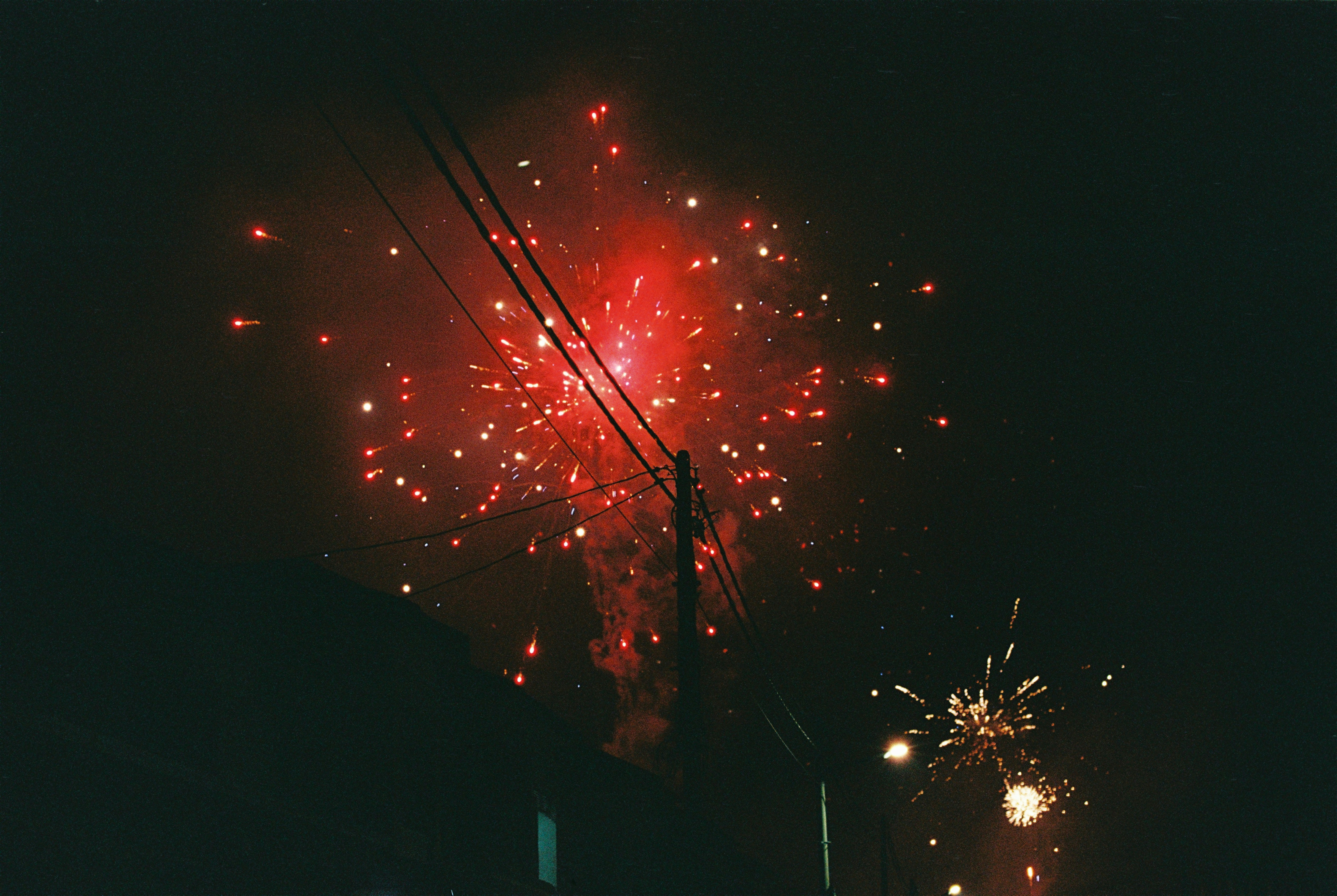 Bright red fireworks exploding in the night sky above a utility pole