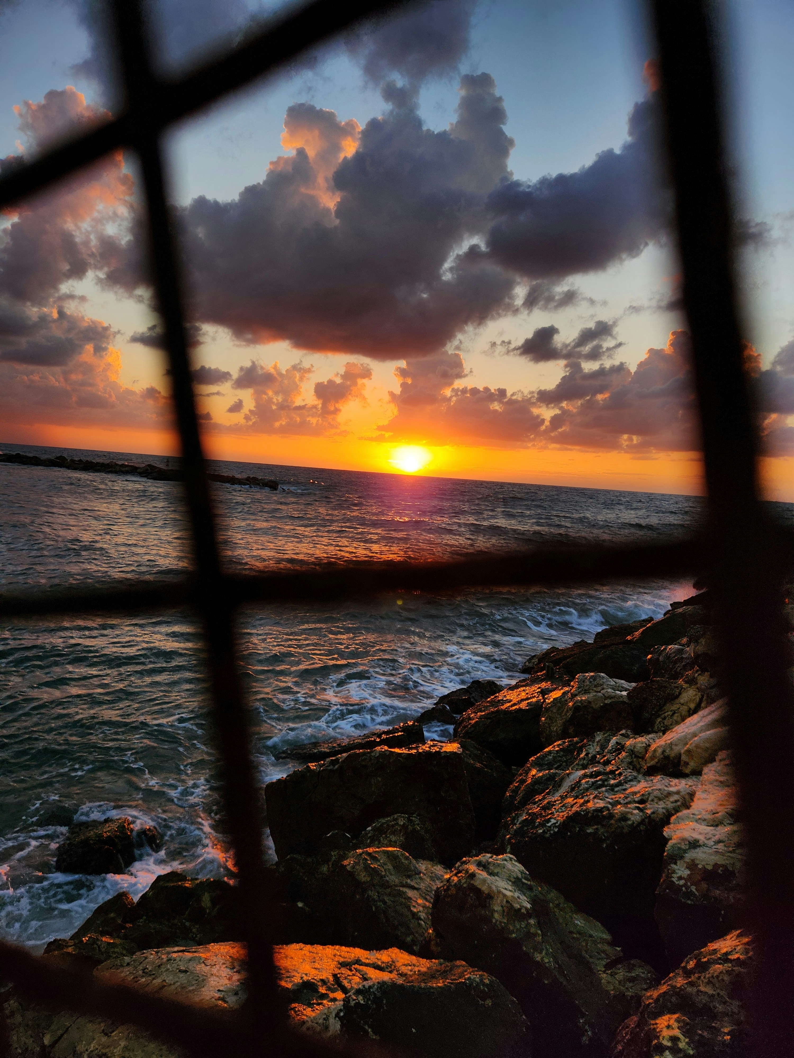 Sunset Through a Guarded Frame: Ocean Rocks and Bars of Light