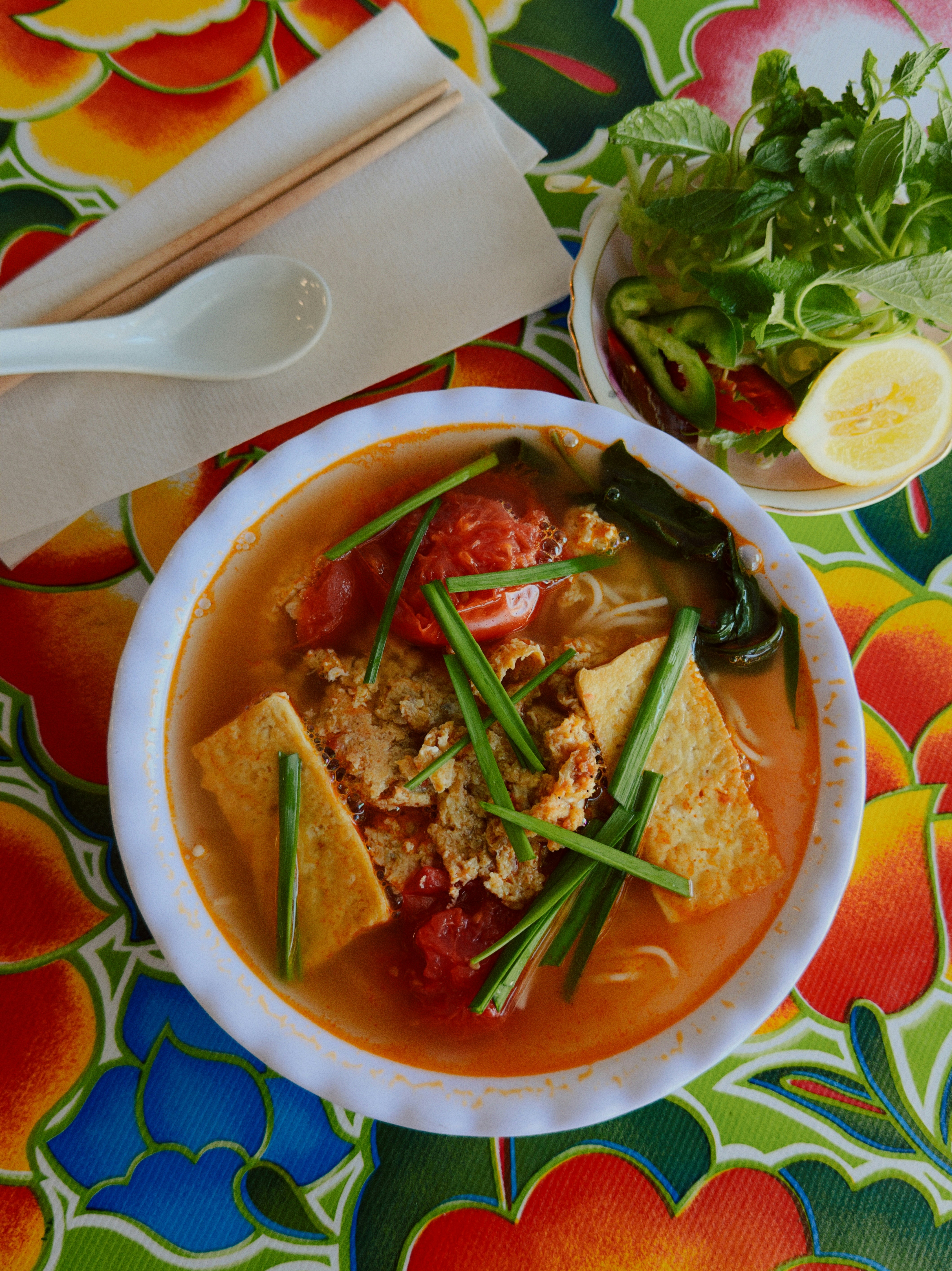Fiery bowl of tom yum with tofu and herbs on a colorful table