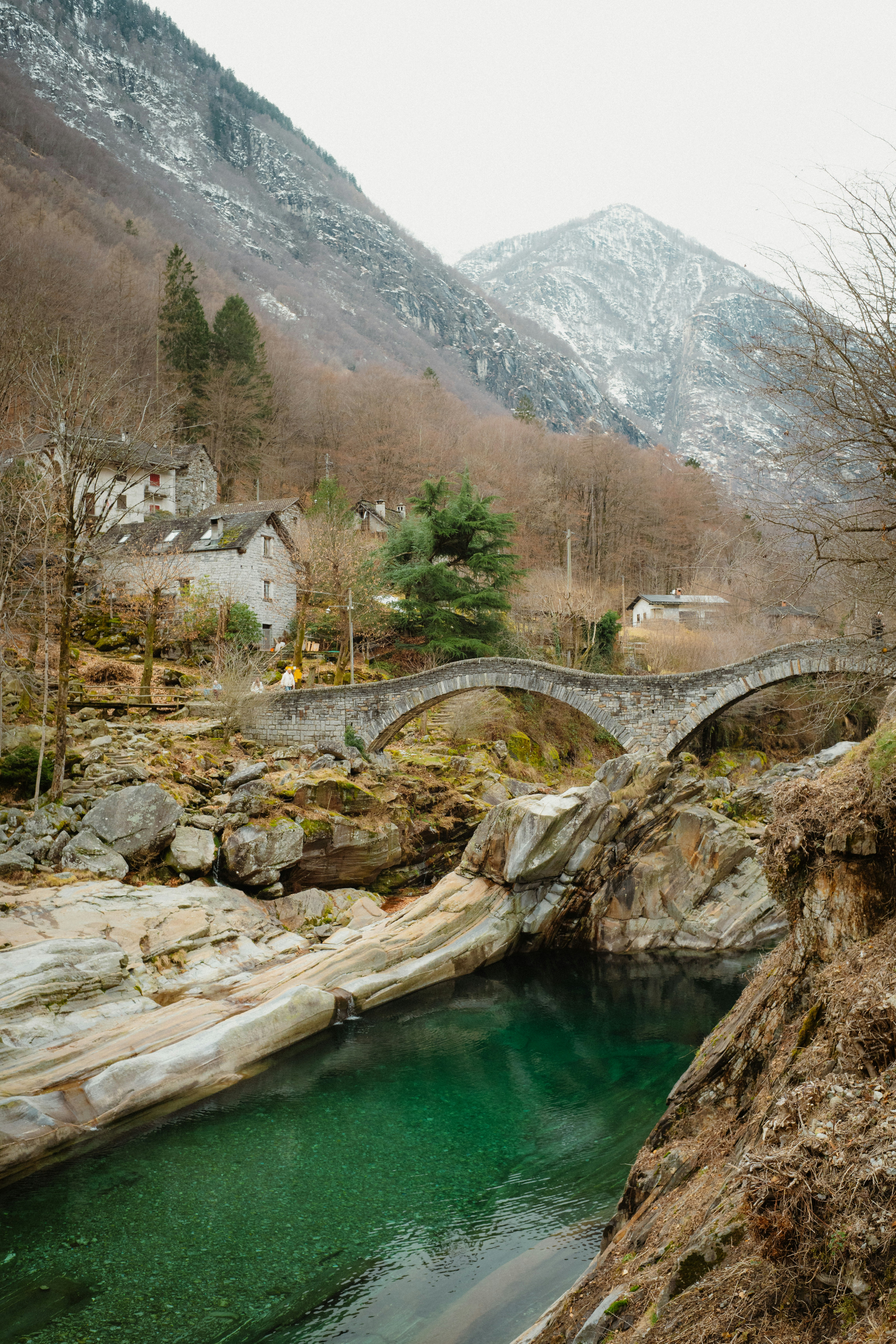 Stone Arch at River’s Edge Under Snow-Capped Peaks