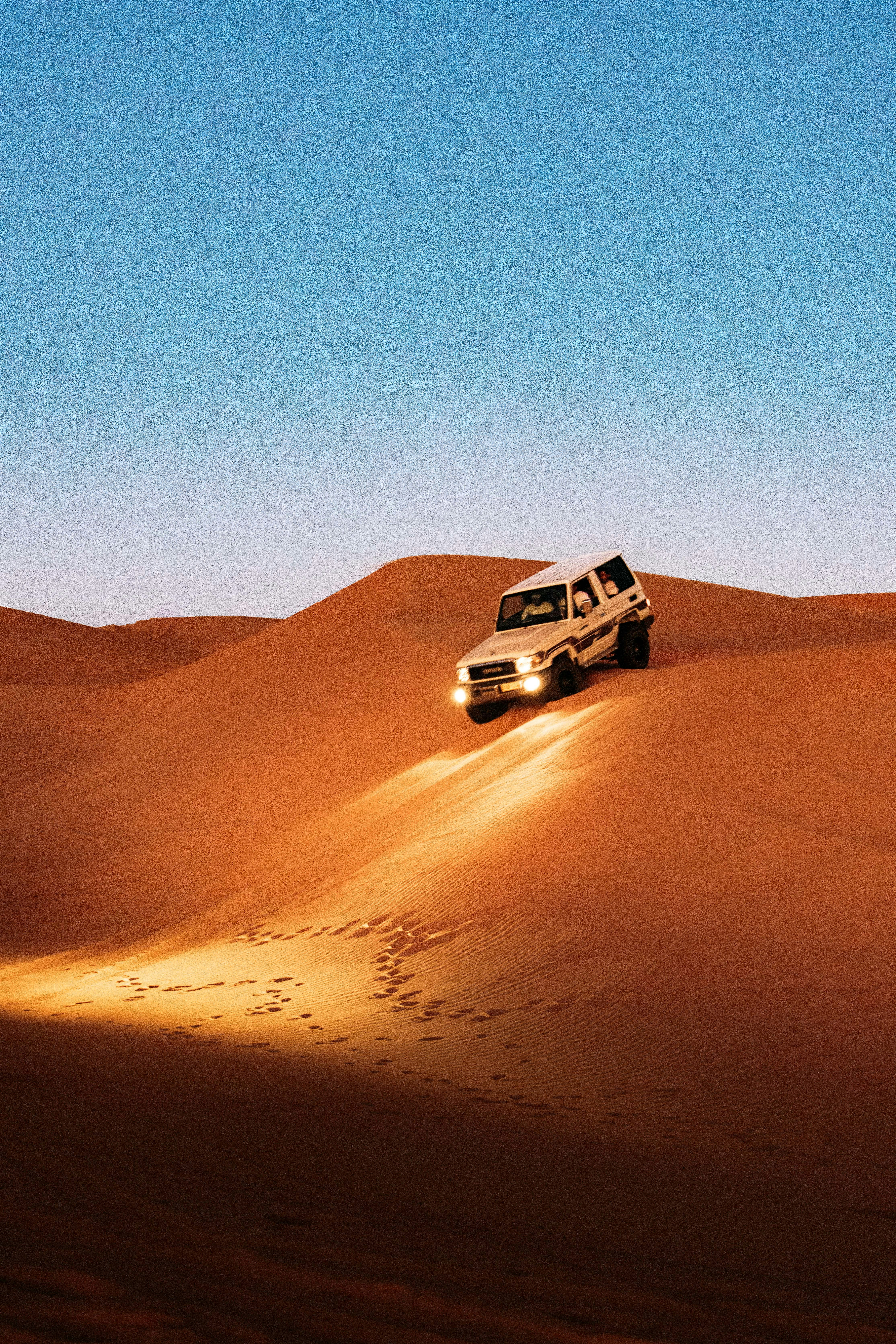 Desert Rally: White SUV Cresting a Dune Under a Clear Sky