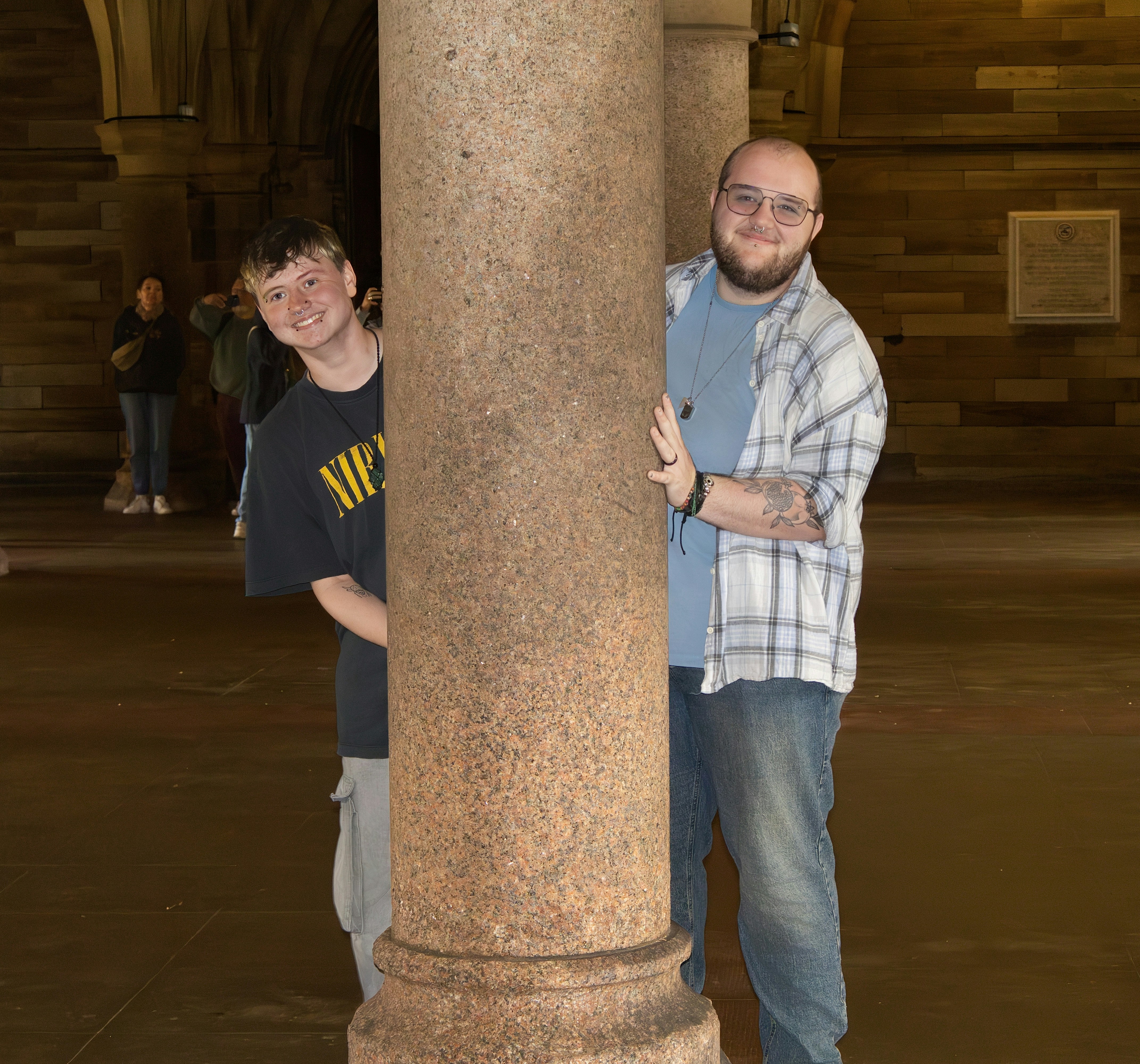 Hidden Duo: Two Friends Peek from Behind a Central Pillar