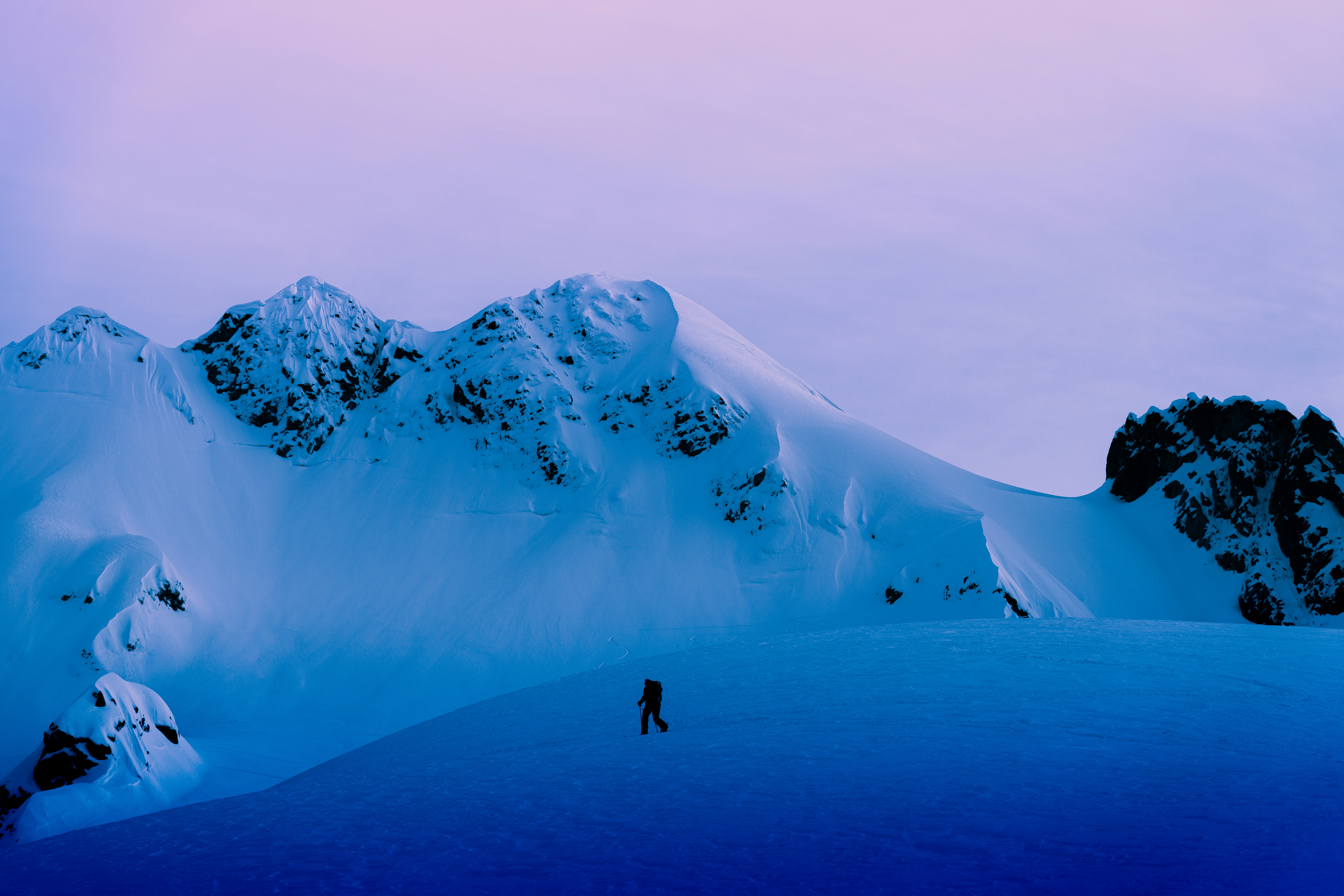 Lonely climber marching under blue-tinted alpine ridges