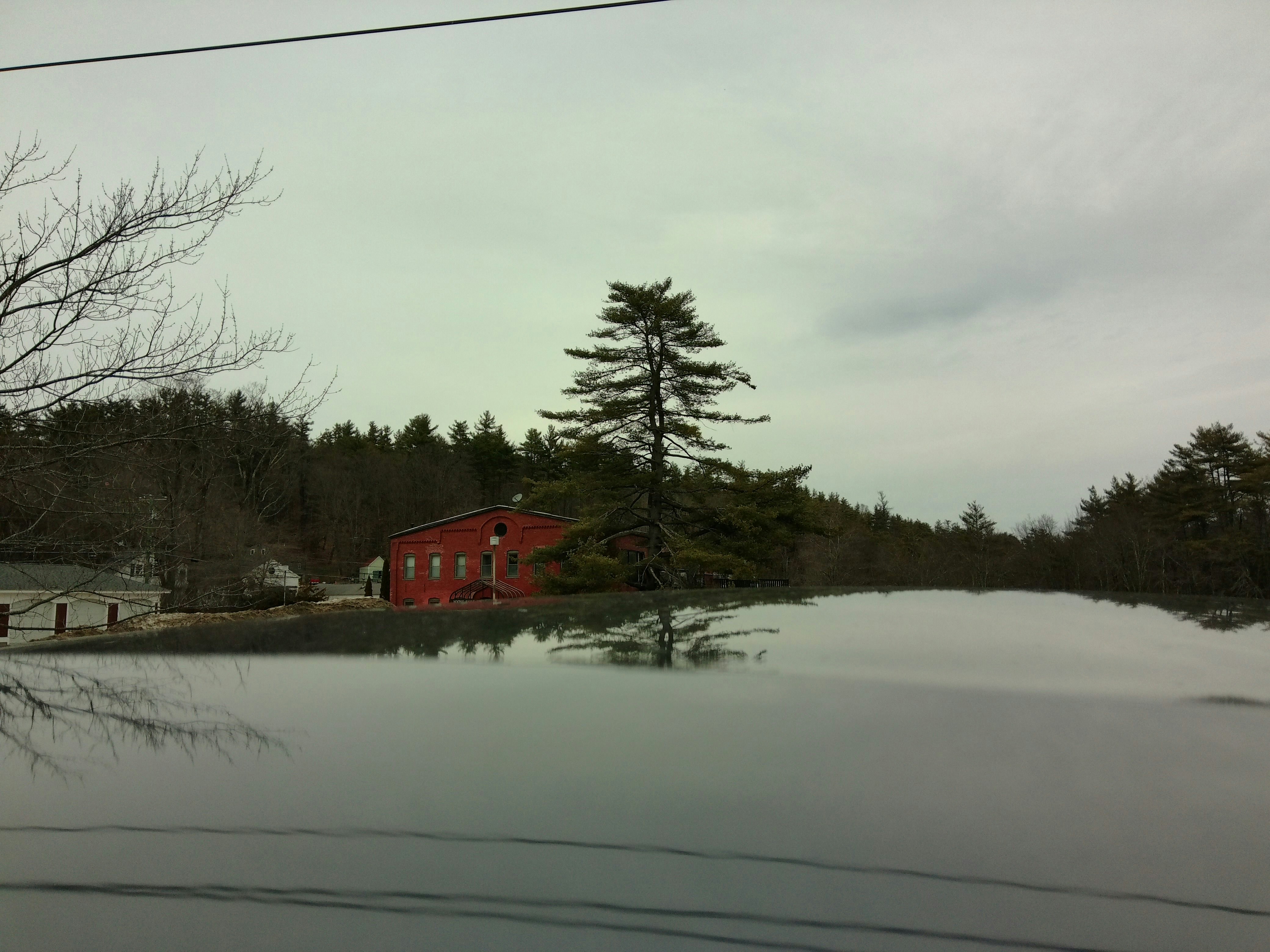A red building, tall tree, and snow under cloudy sky.