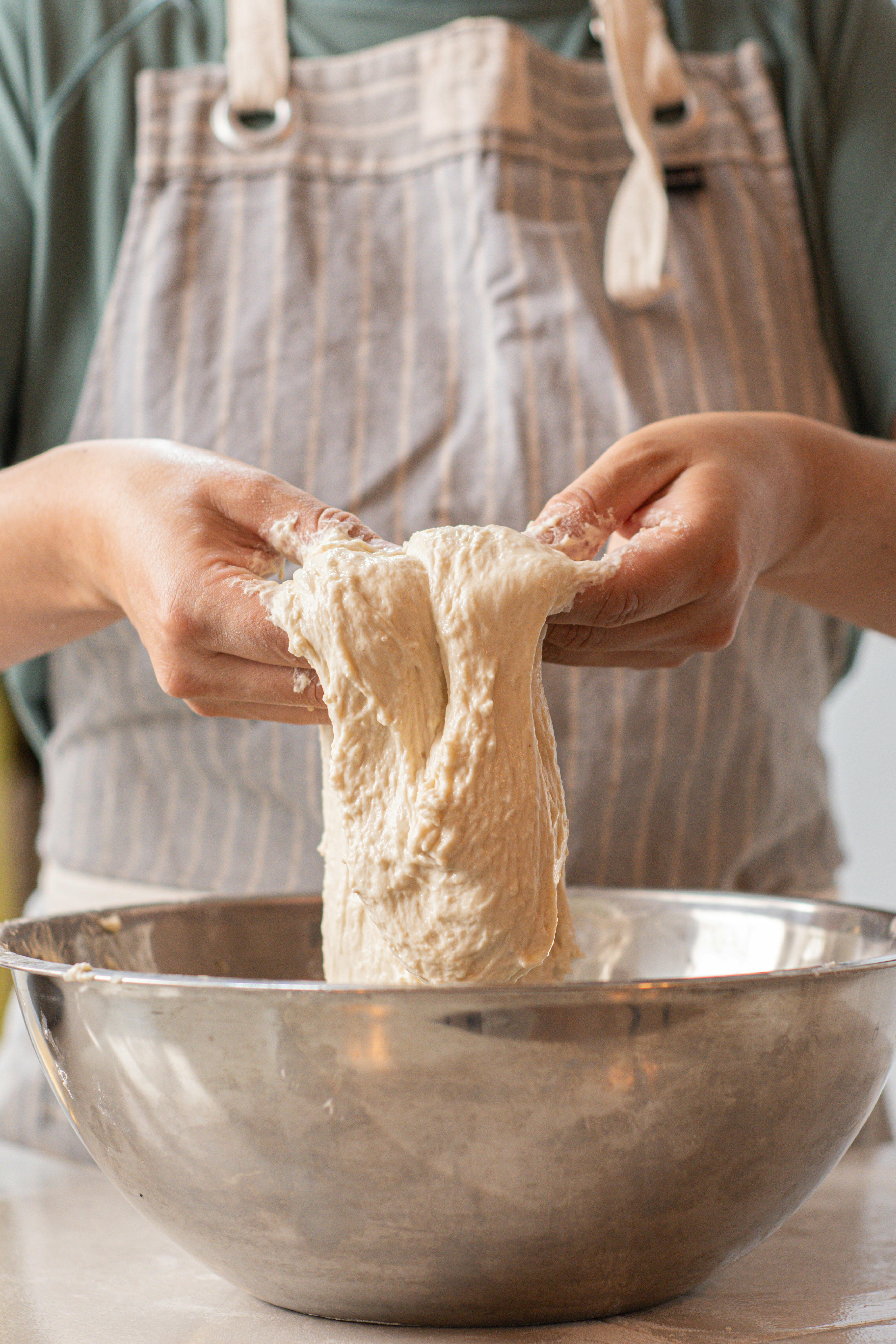 Kneading Protein: Hands Stretch Dough Over a Stainless Bowl