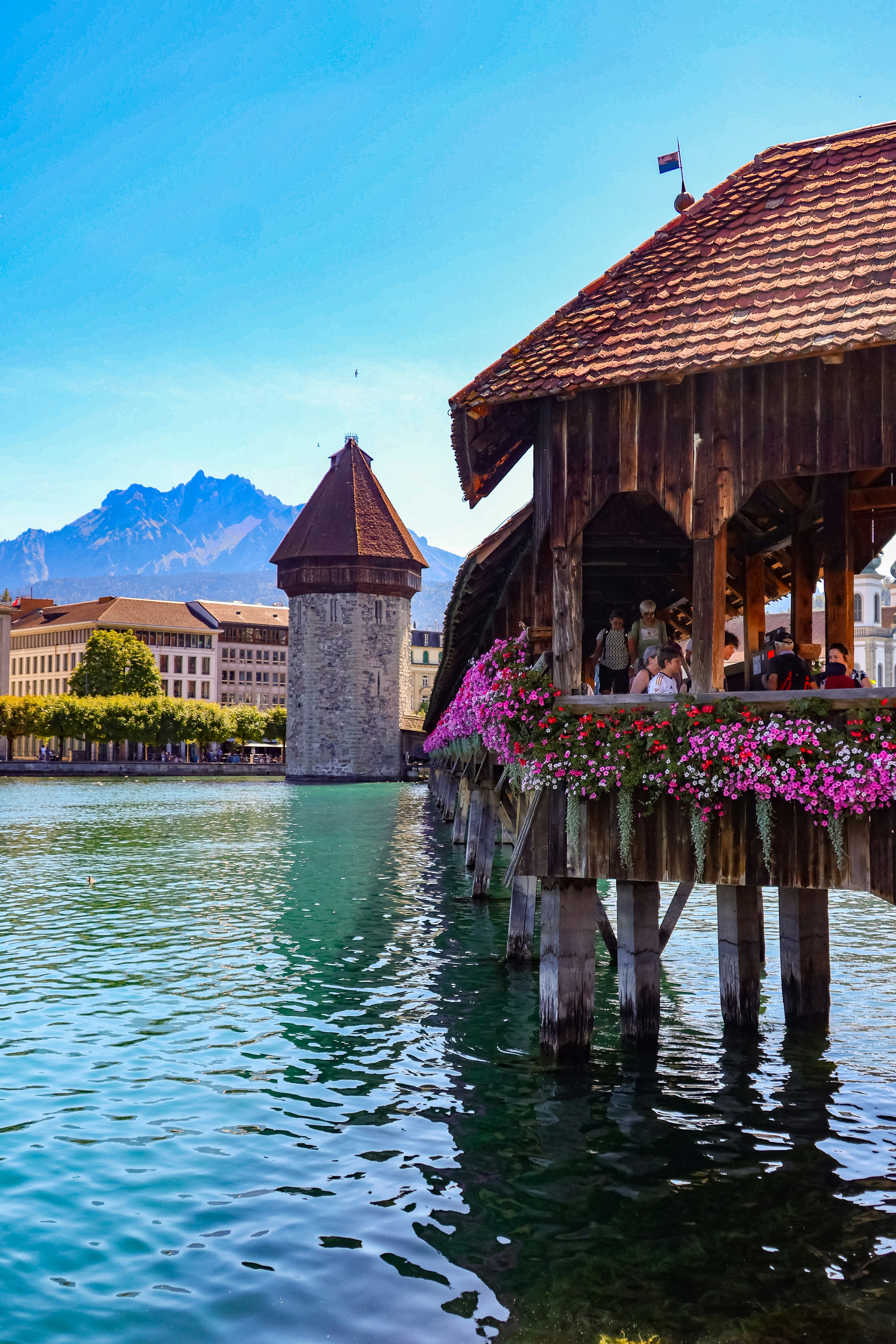 Wooden pavilion over turquoise lake with distant castle tower and alpine backdrop