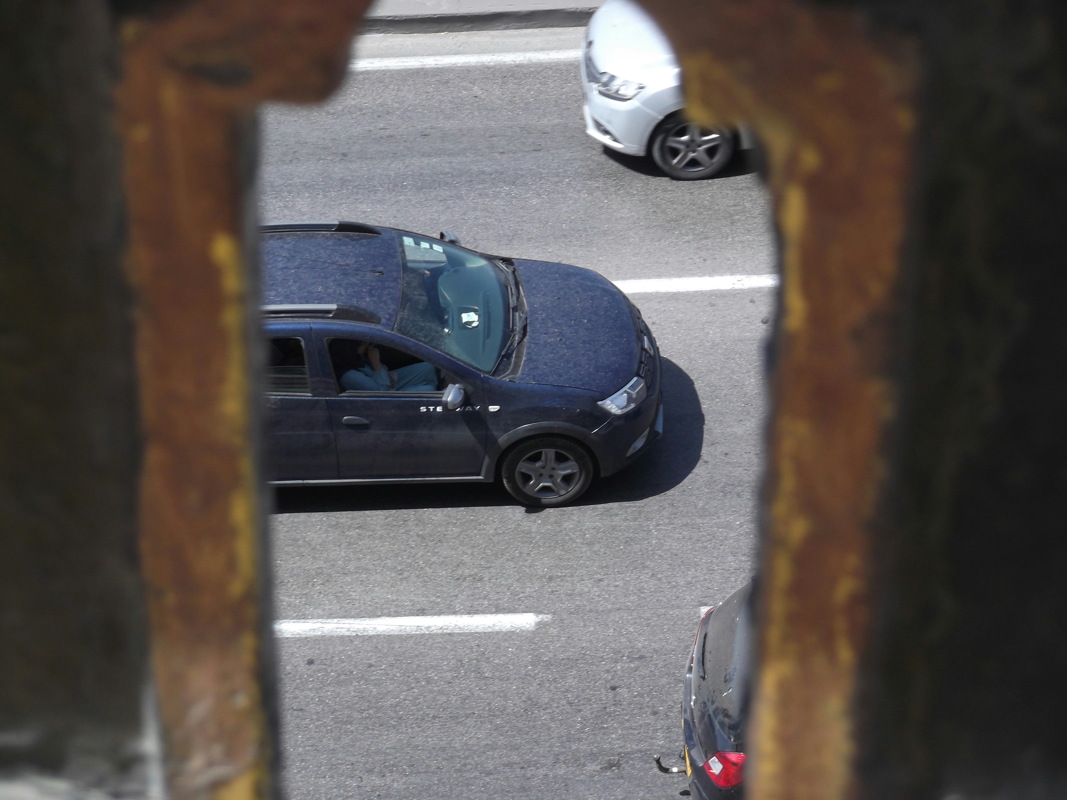 Framed through a industrial aperture: a dark taxi travels along a sunlit street