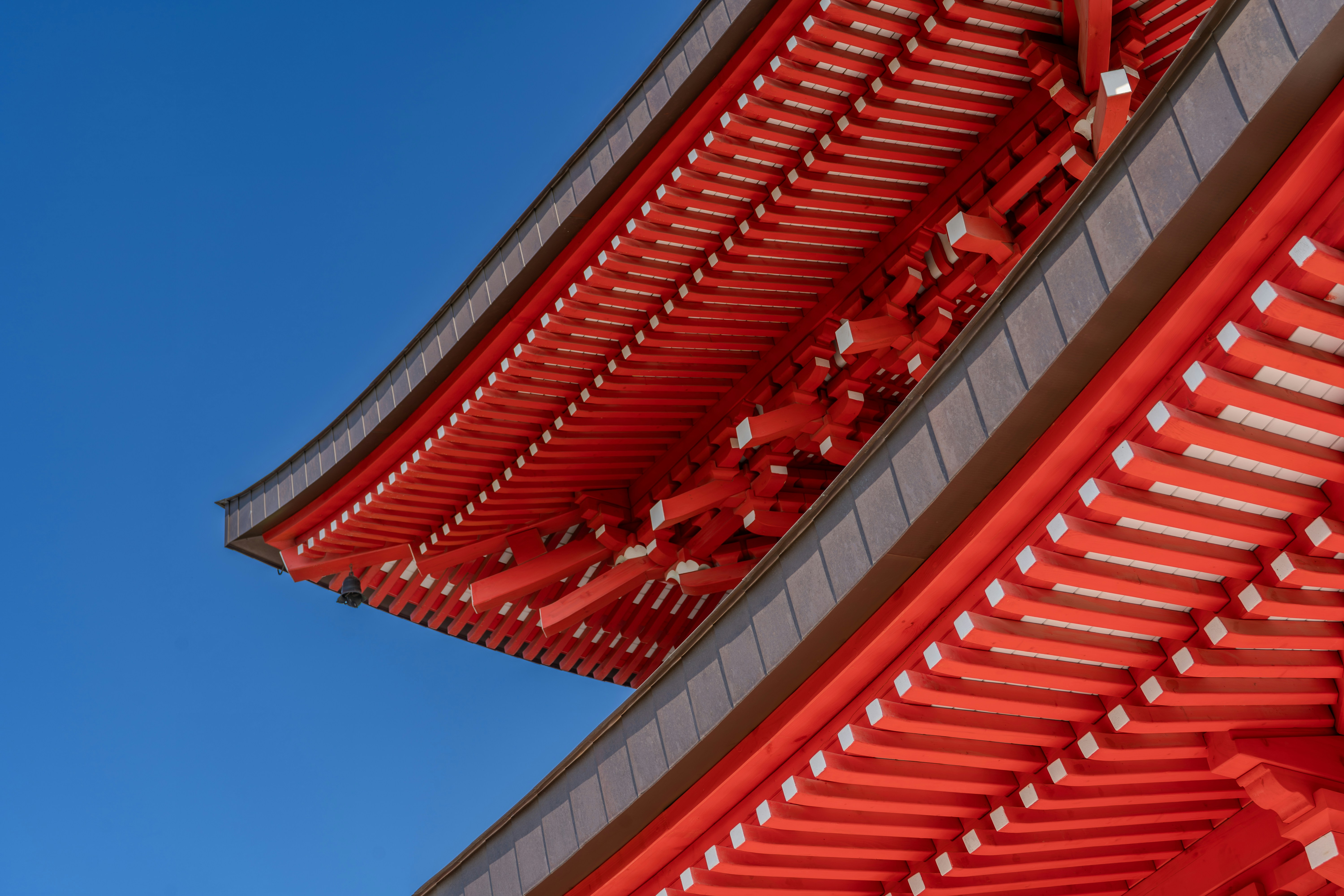 Architectural detail of a vivid red roof structure set against a blue sky, revealing repeating beams and supporting elements. (Photo type: architectural detail.)