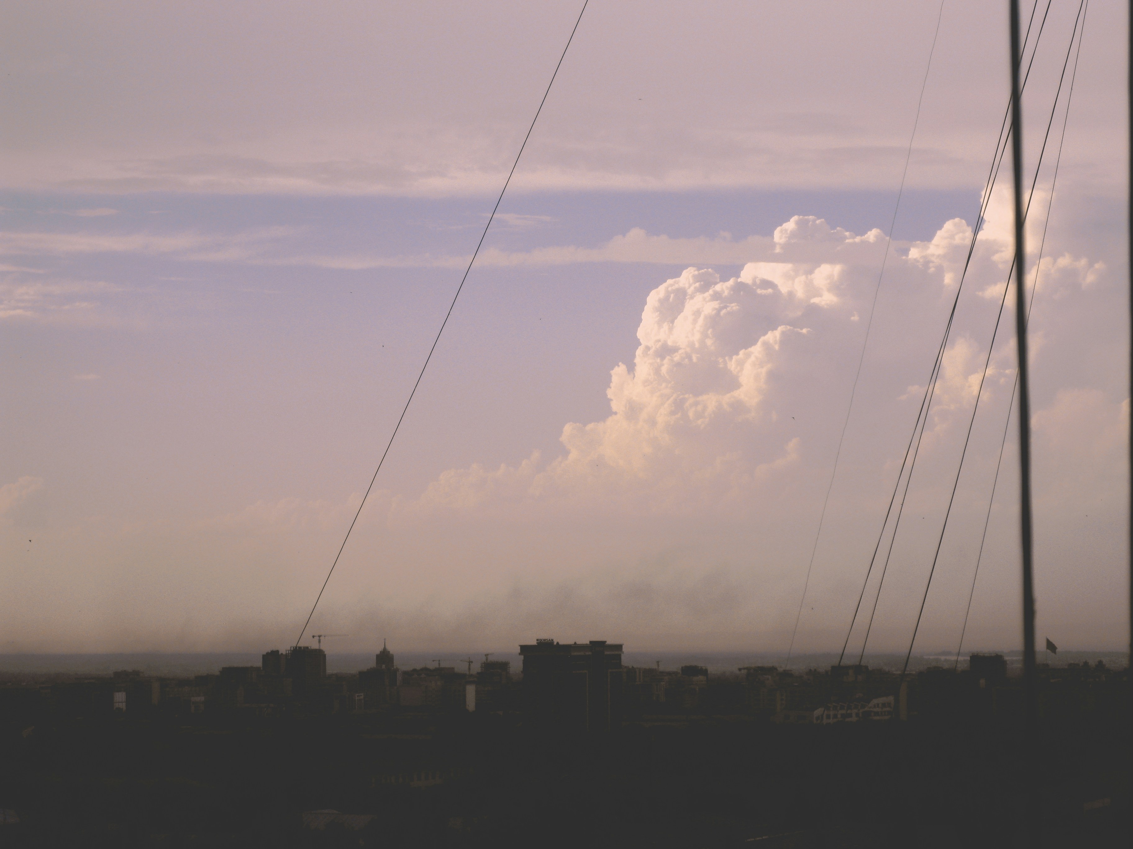 Vast cloudy sky above a city silhouette and wires.