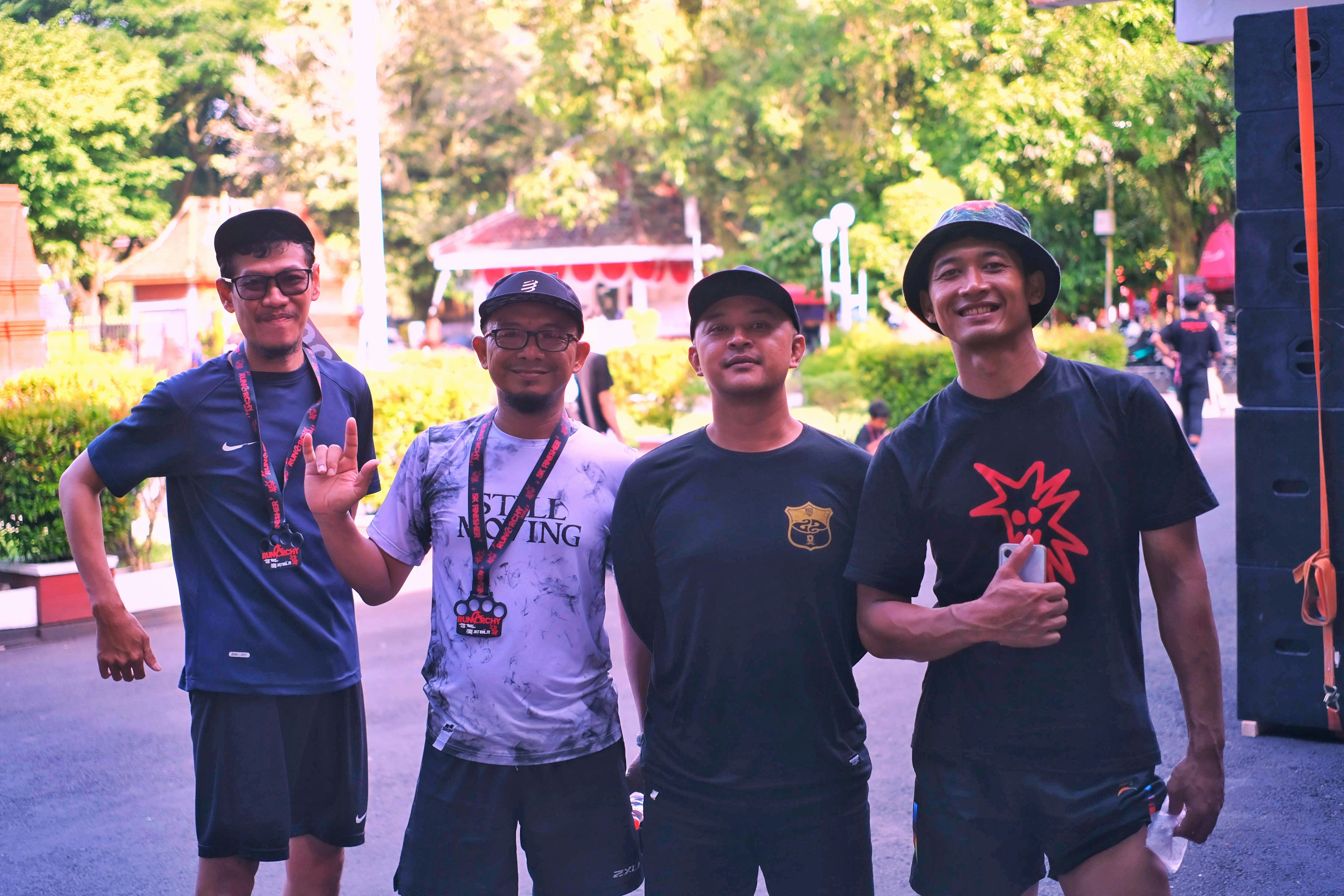 Four friends posing at an outdoor festival, sunlit smiles and casual gear