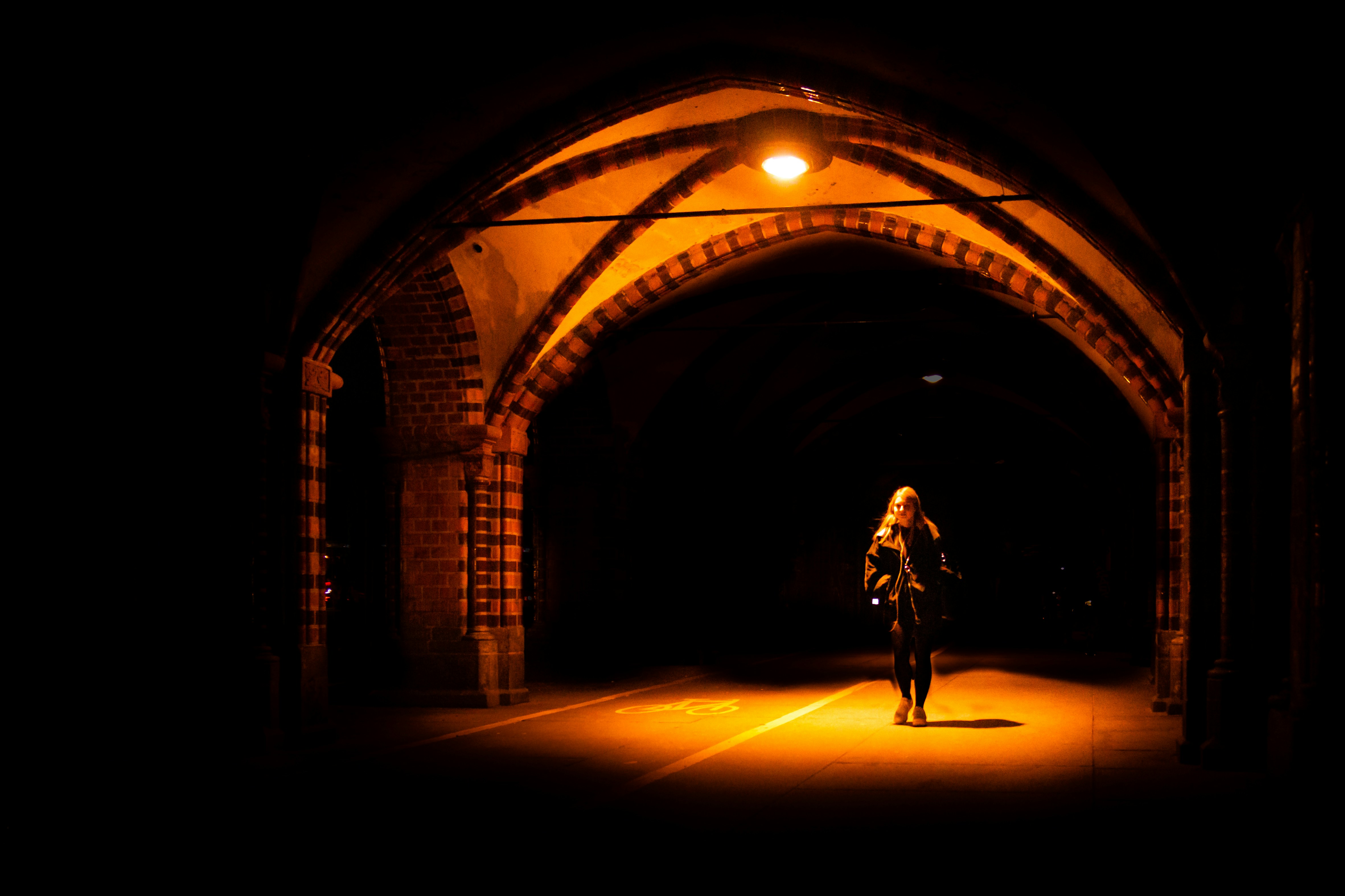  solitary figure under orange glow in brick-arched tunnel