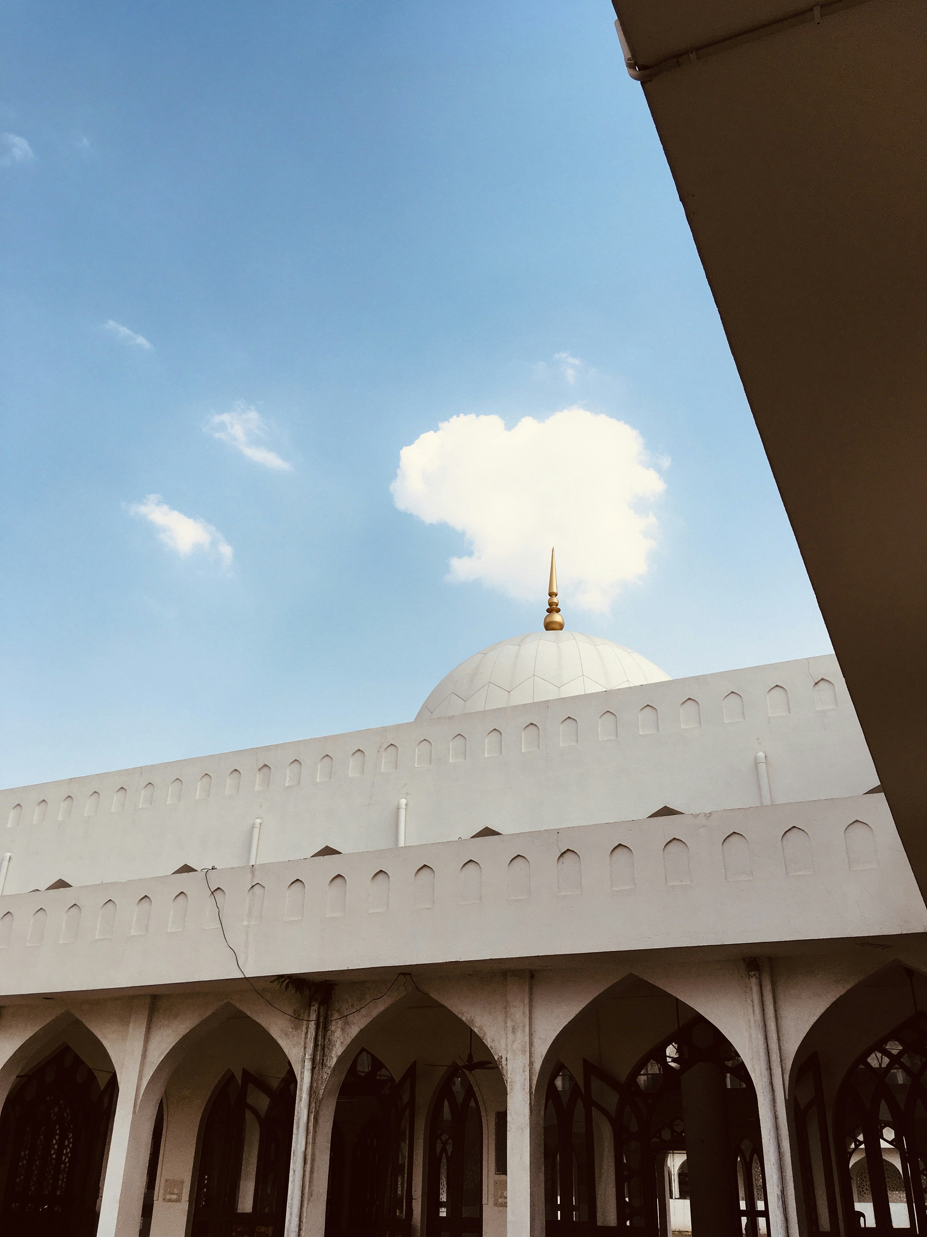 White domed mosque facade against a bright blue sky with arches at the base; a hint of architectural rhythm and shadow defines the scene.