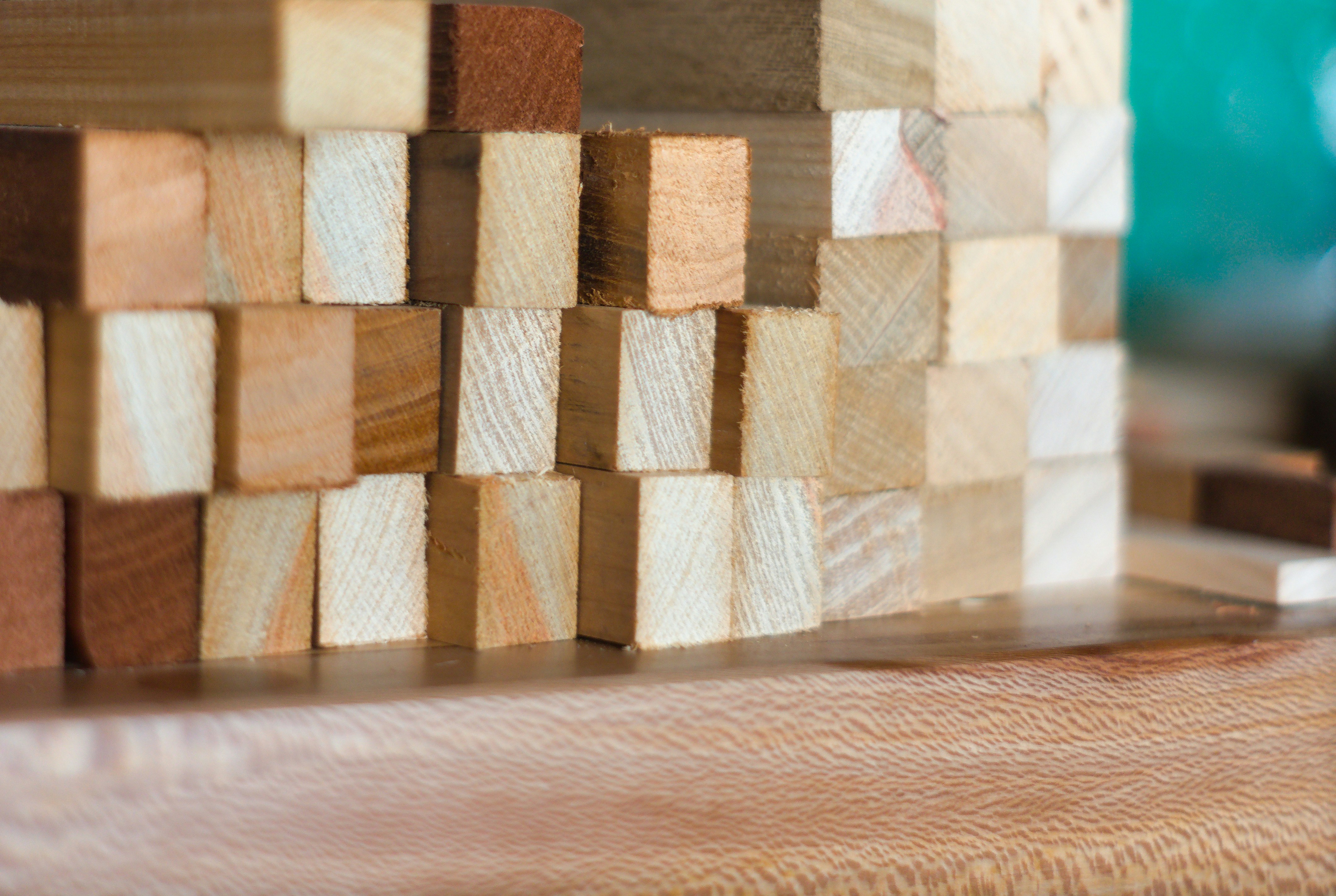 A close-up of stacked wooden blocks on a workbench, highlighting the geometric grain and pale wood tones. This is a detailed wood-block arrangement with a blurred background.